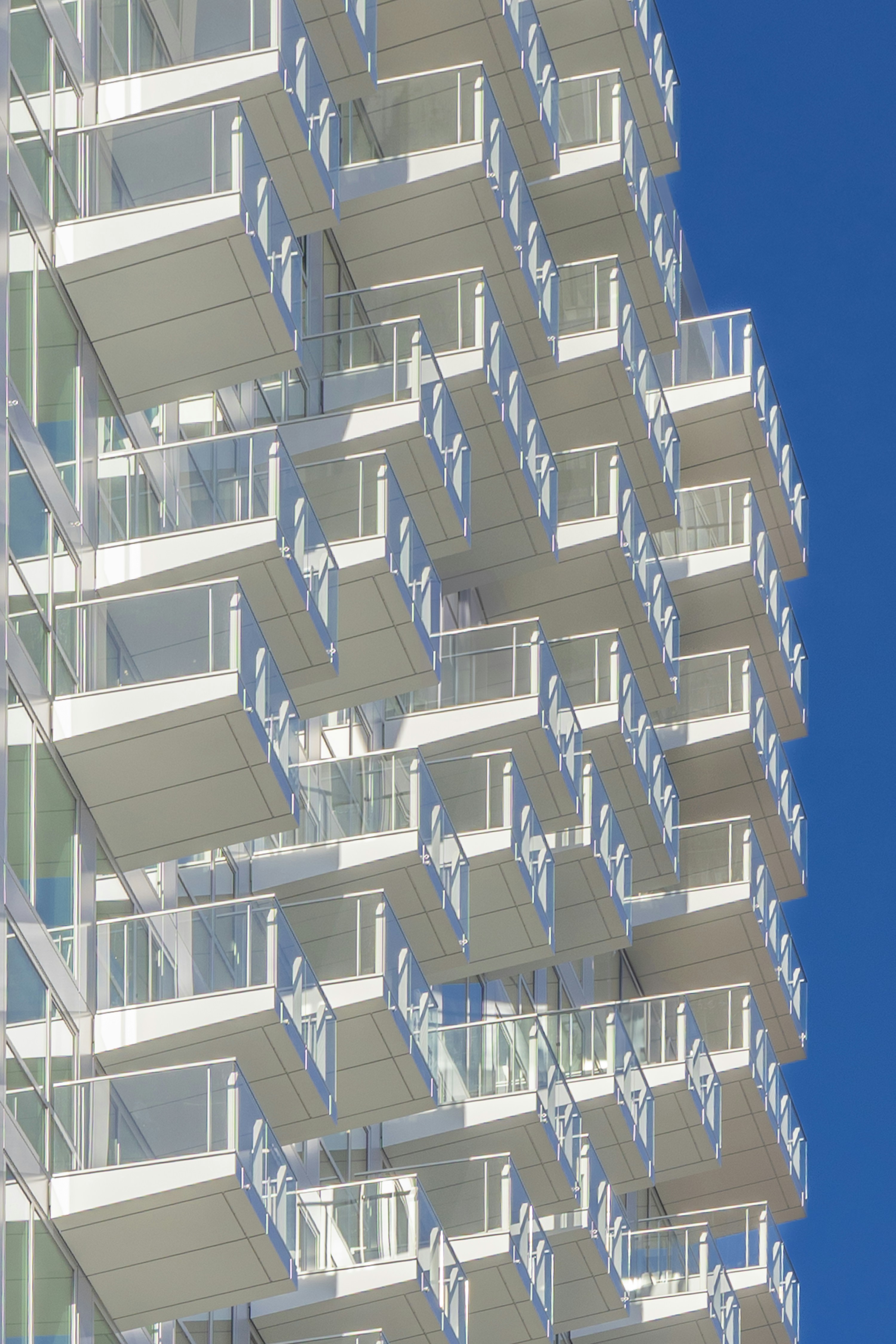 Modern apartment building with staggered balconies set against a clear blue sky.