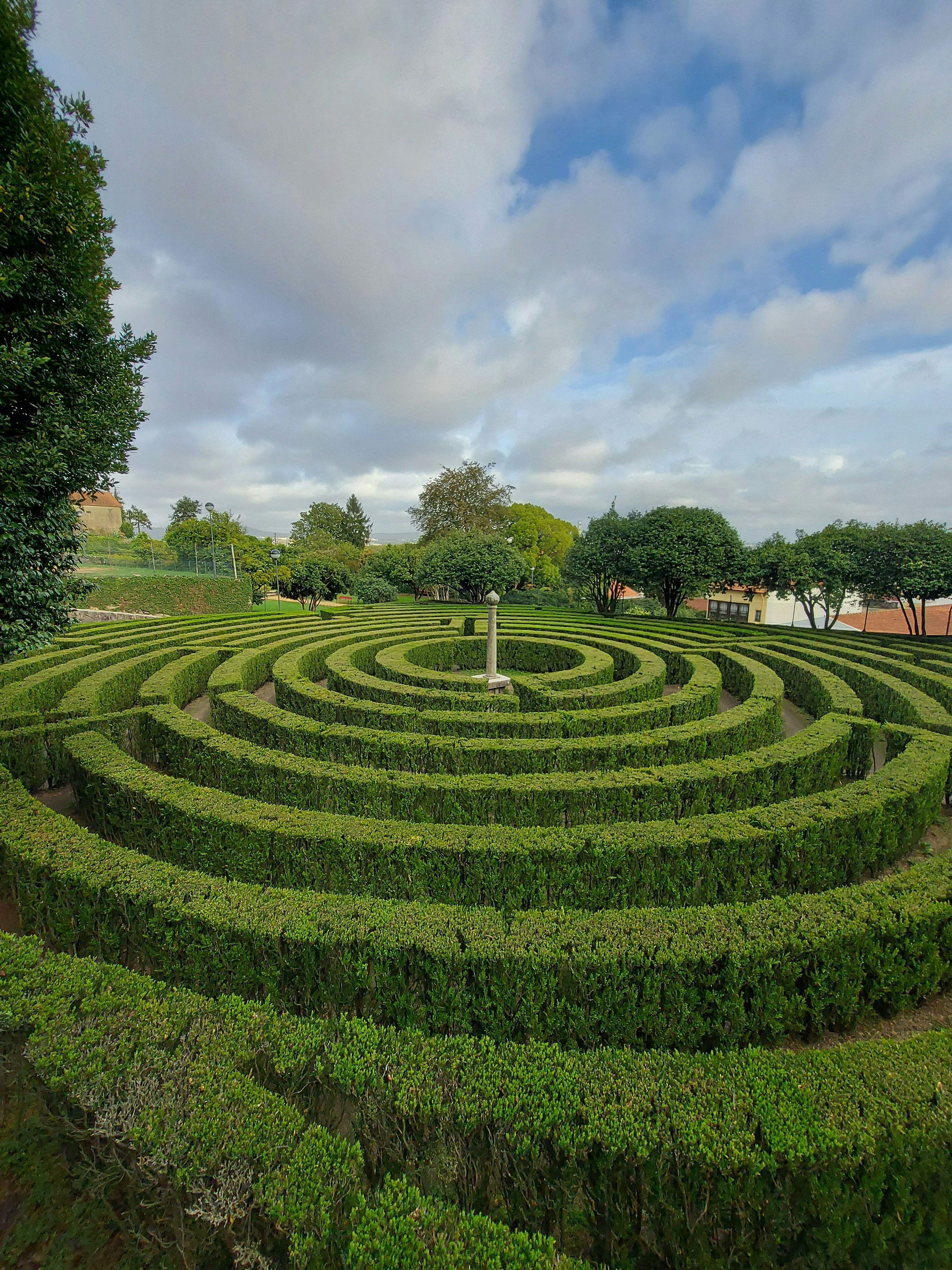 Circular hedge maze with concentric circles under a partly cloudy sky.