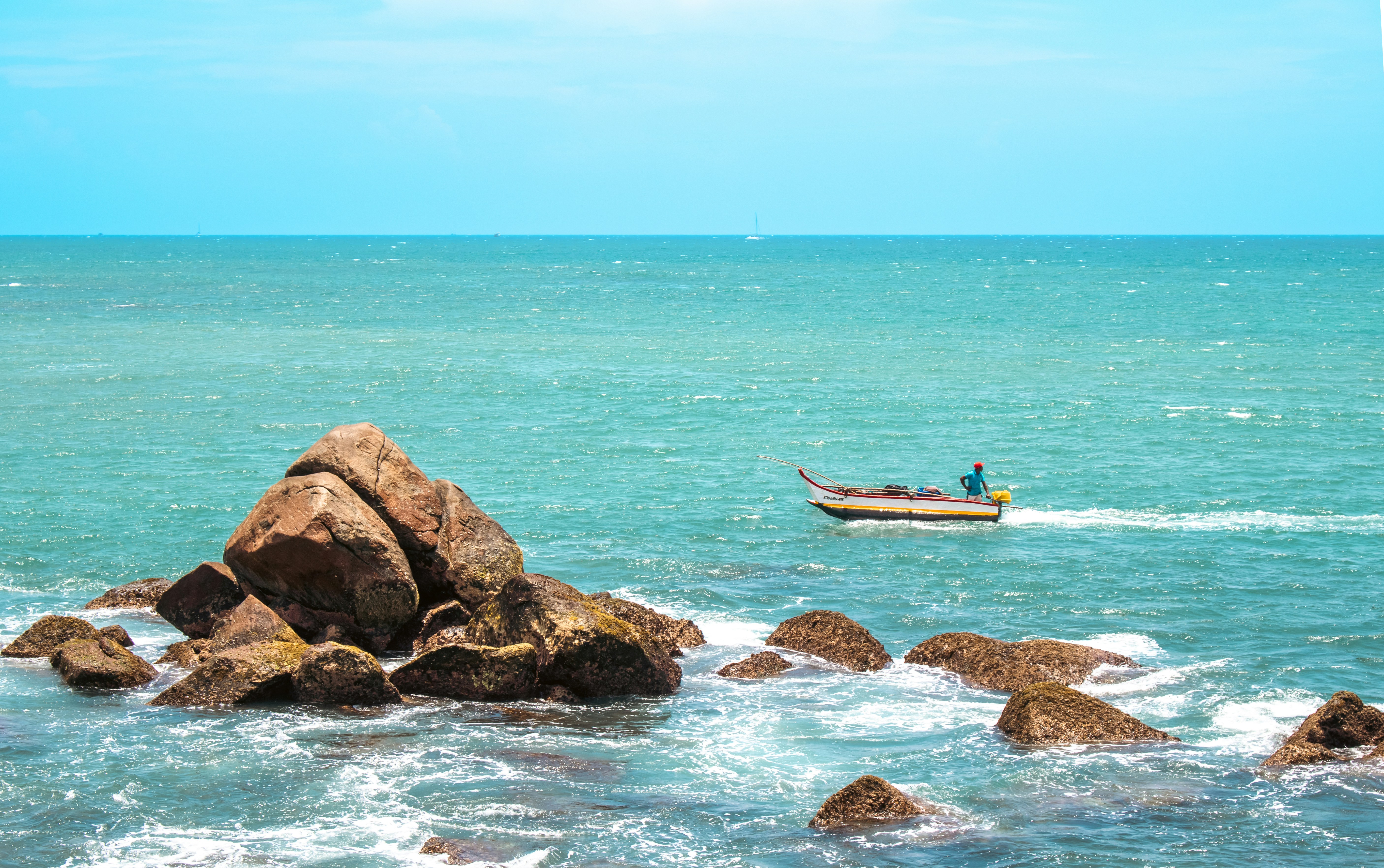 Rocks and a boat sailing across the turquoise sea. photo – Free Travel ...