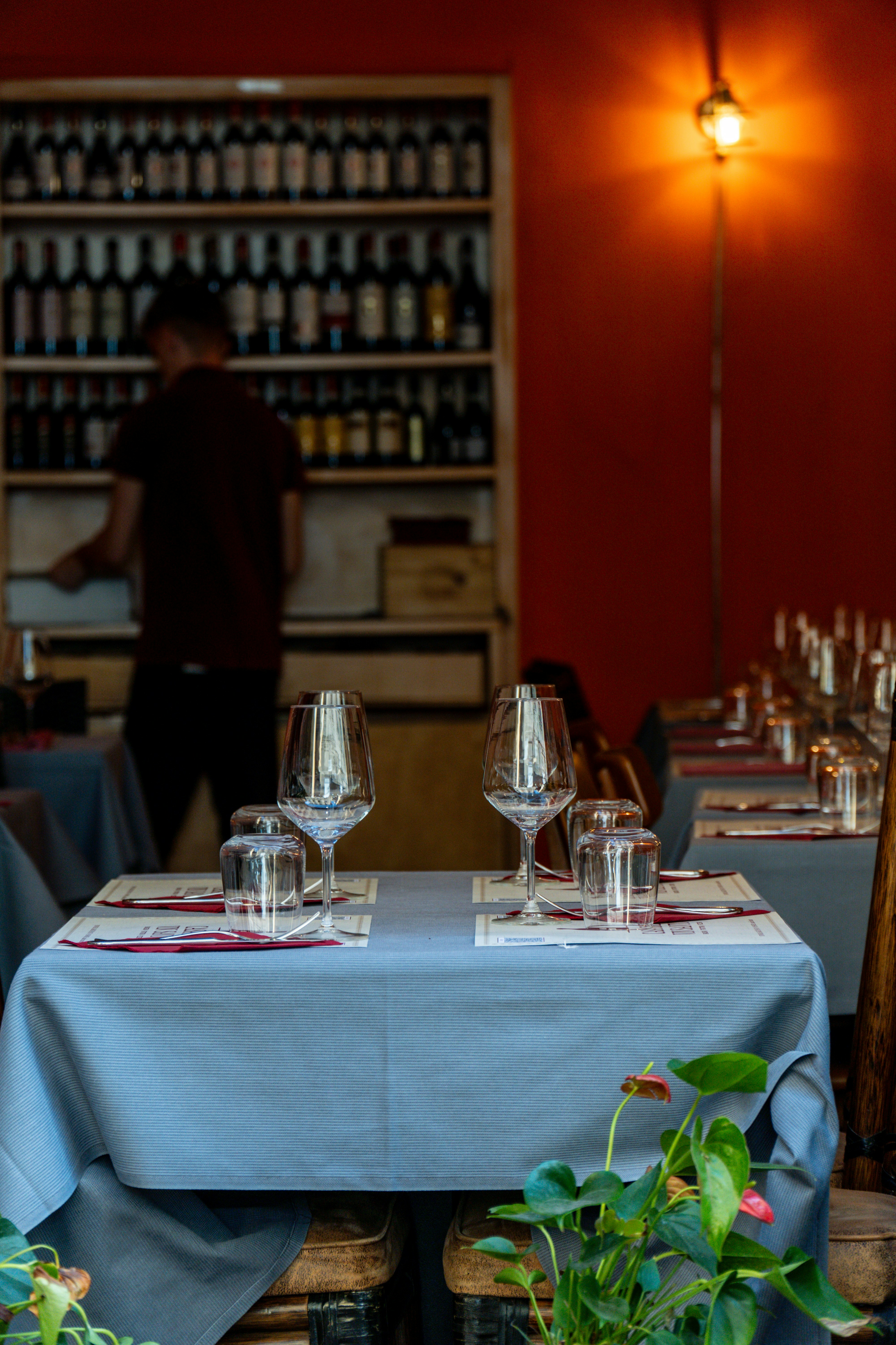Elegantly set table in a cozy restaurant with warm orange walls and a wine shelf in the background.
