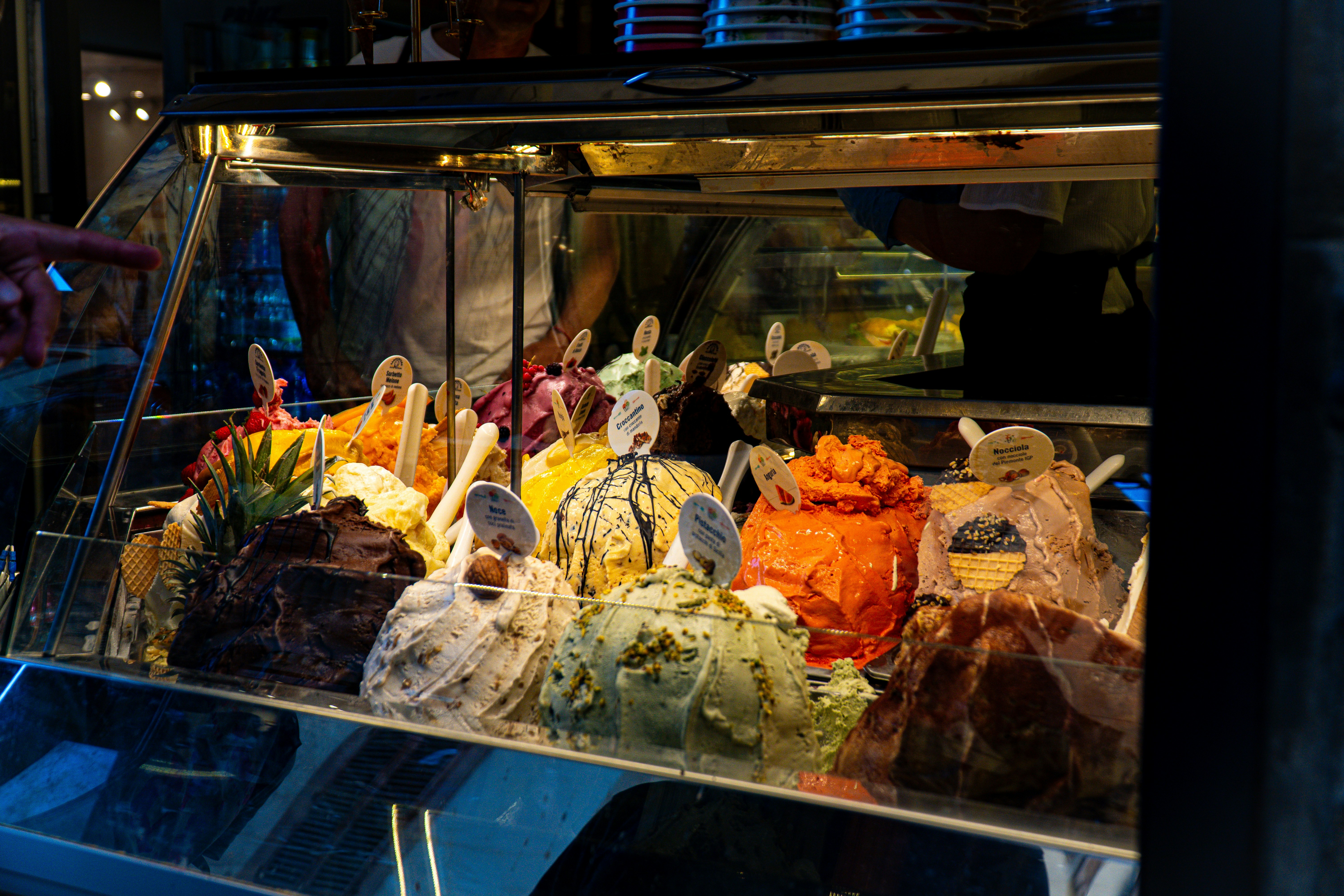 Variety of colorful gelato flavors arranged in a glass display case under warm lighting.