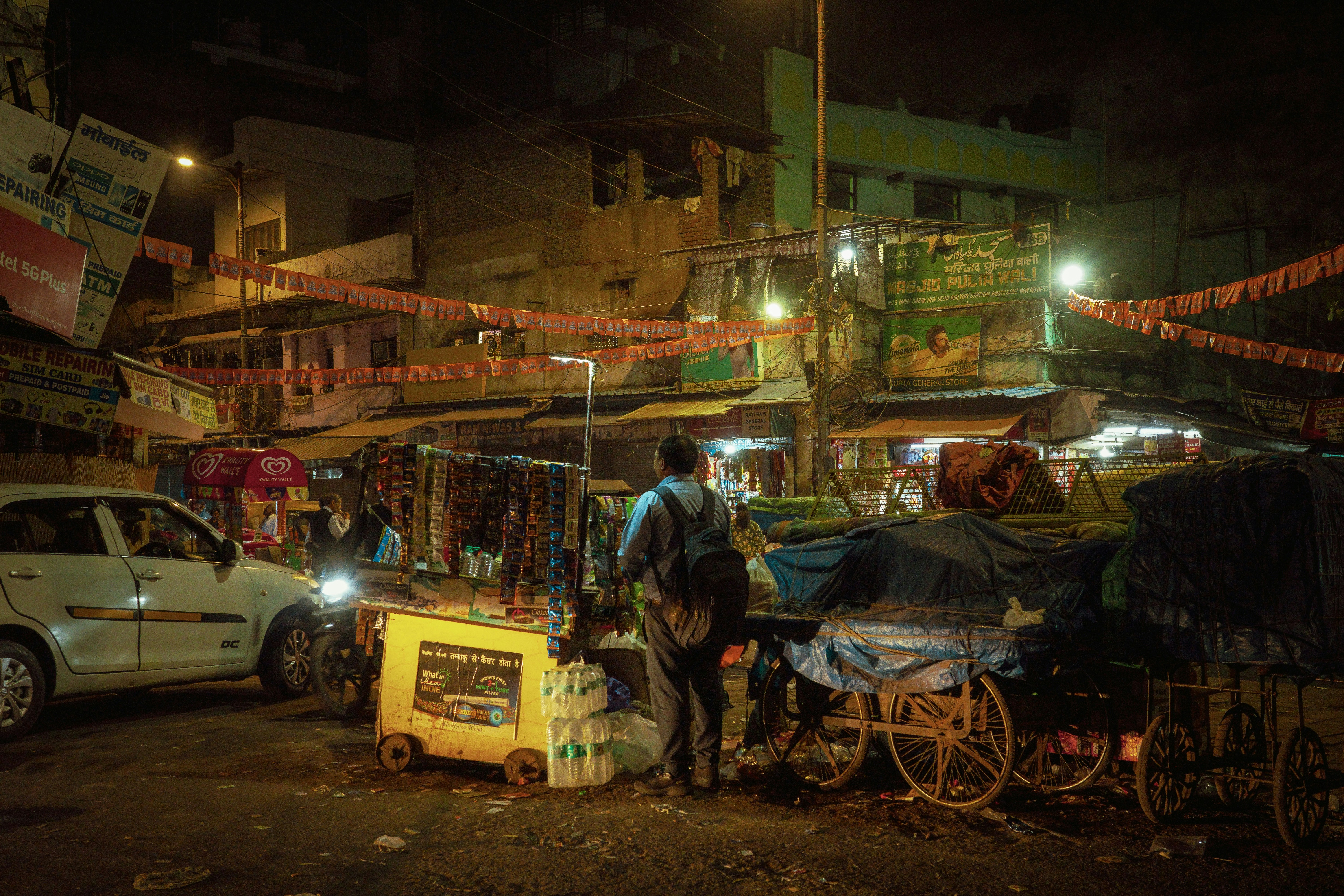 Bustling street market at night with vibrant lights and diverse stalls, surrounded by colorful buildings.