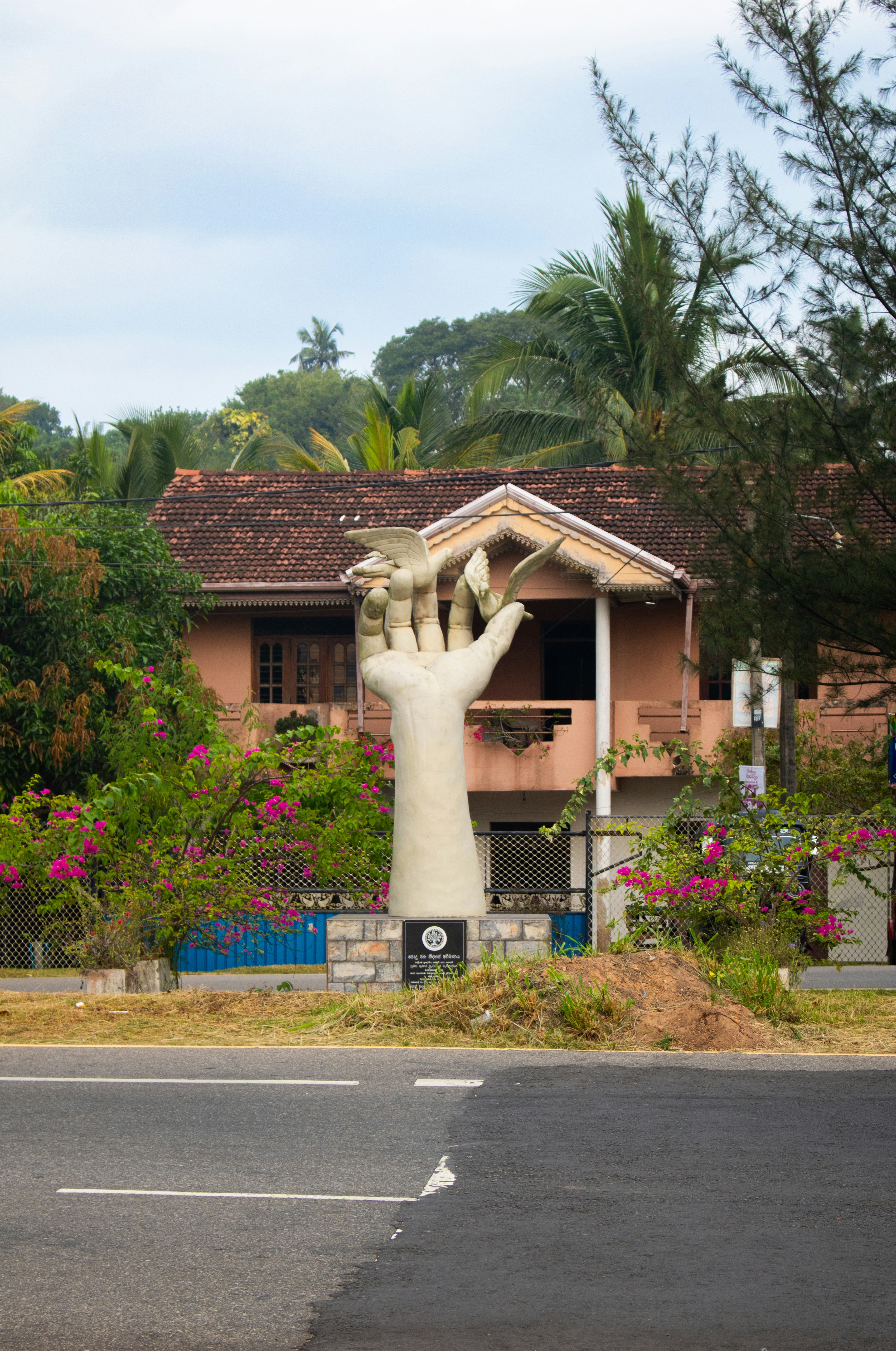 Concrete sculpture of a large hand releasing three doves stands beside a suburban road.