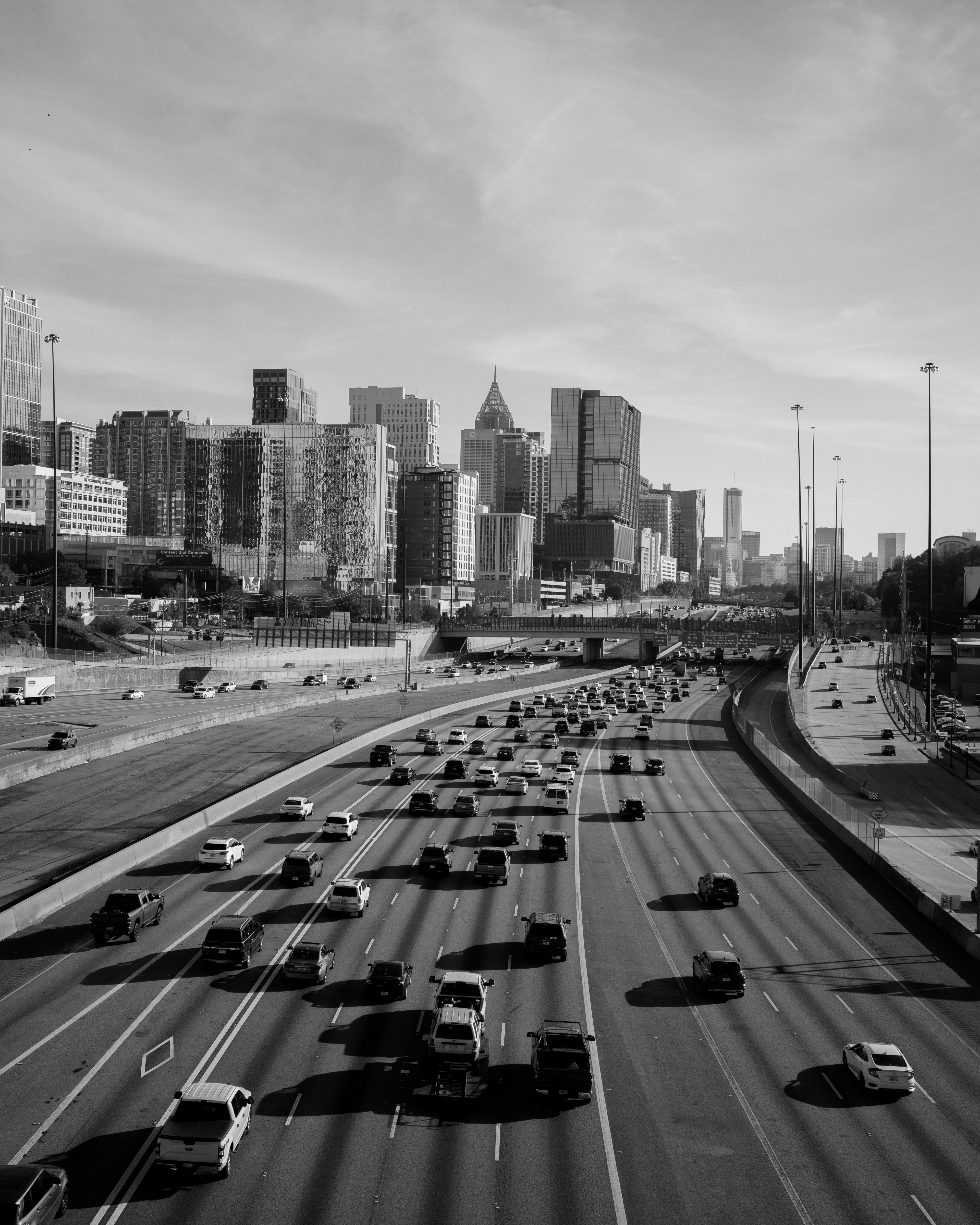 A bustling highway scene with a dynamic flow of vehicles, framed by a skyline of modern architecture in monochrome.