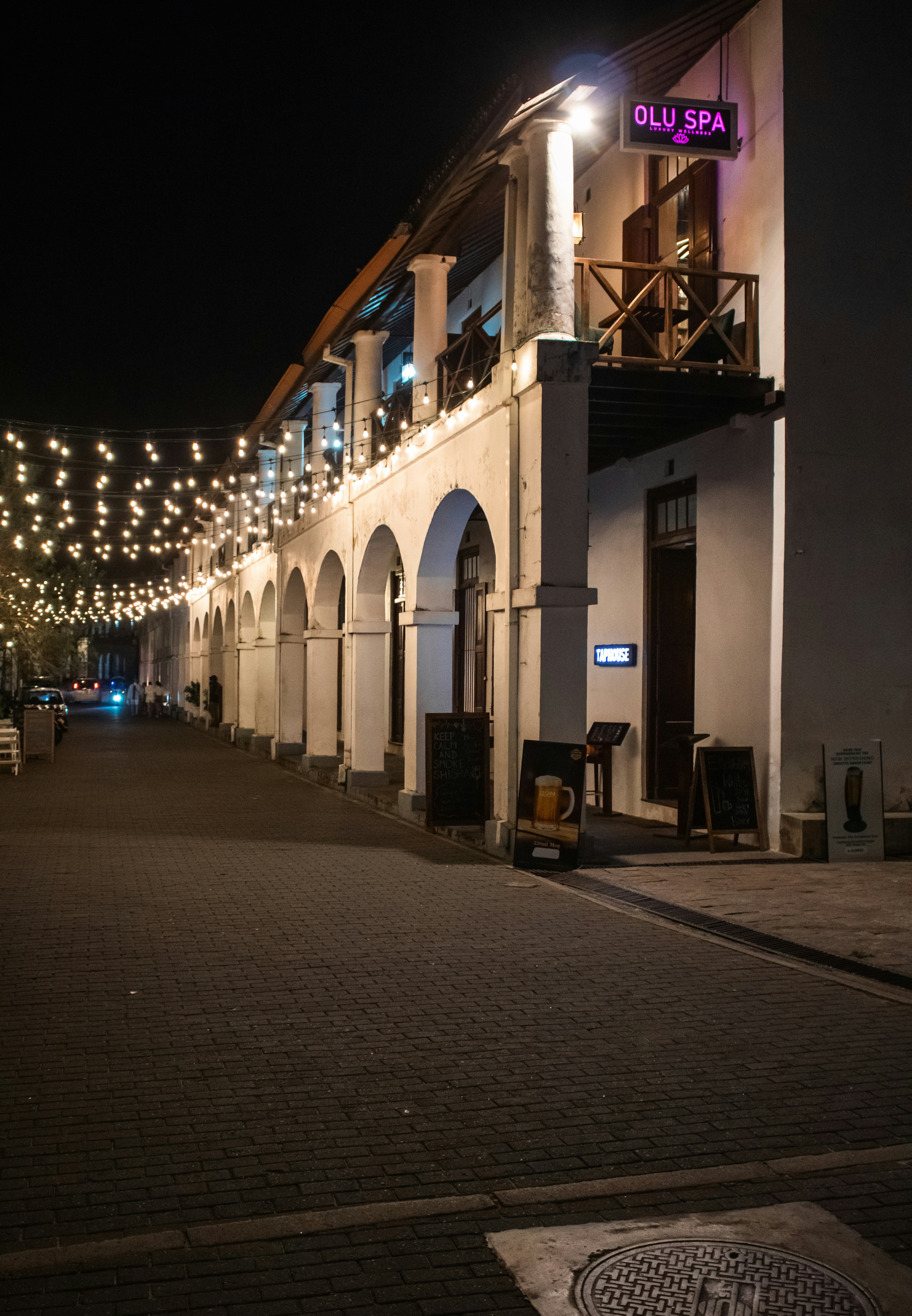 Colonial-era building with arched walkways illuminated by string lights at night.