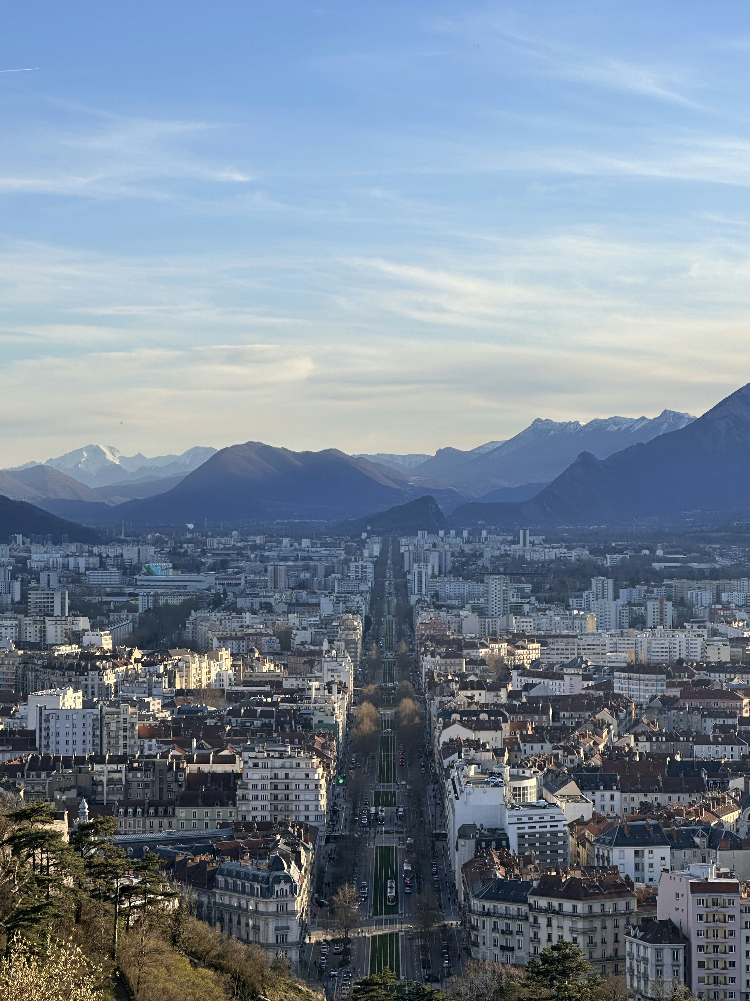 A panoramic view of a cityscape framed by towering mountains, showcasing a vibrant urban layout and clear sky.