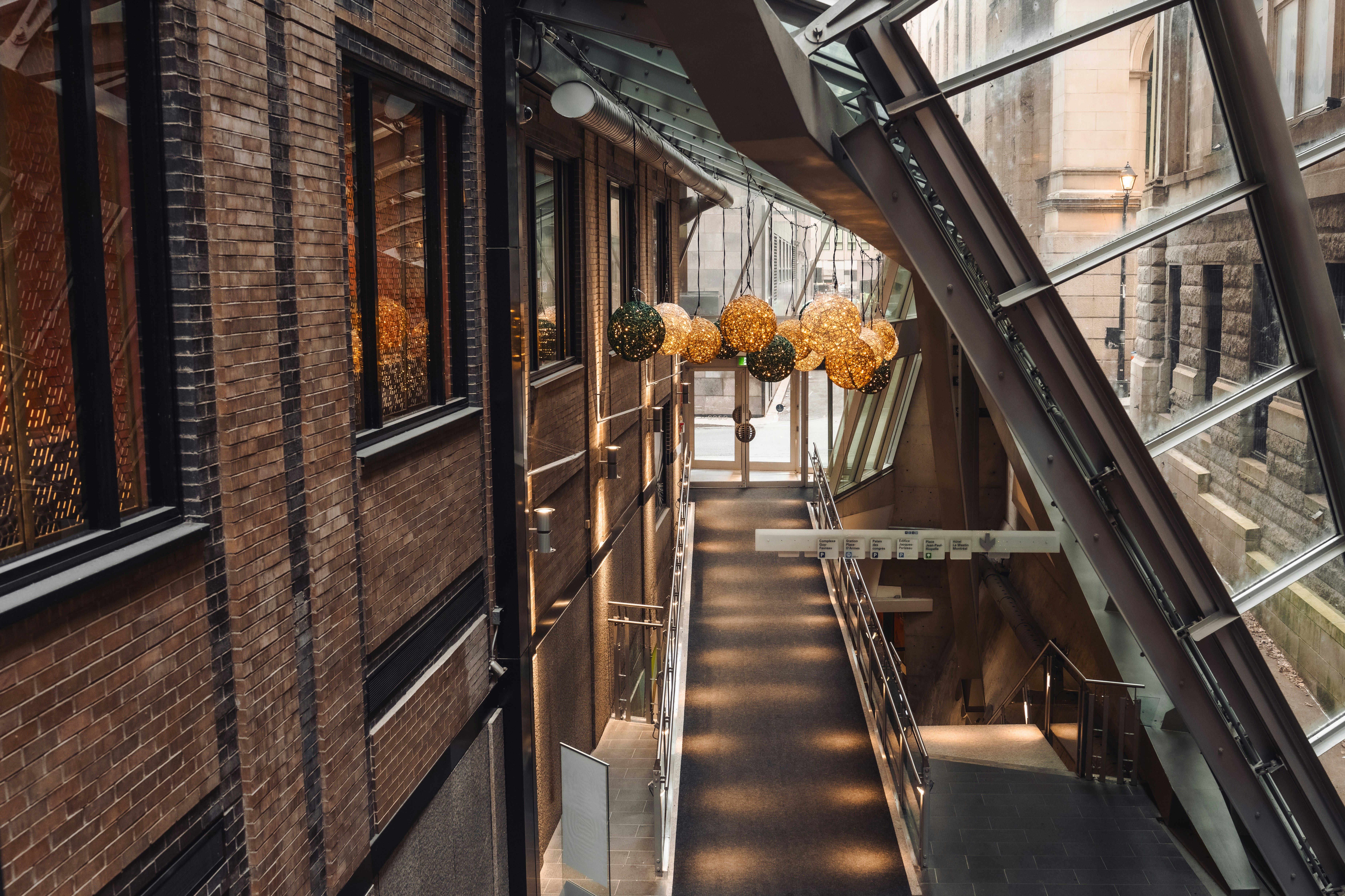 Modern architectural corridor with glass and brick elements illuminated by warm lighting.