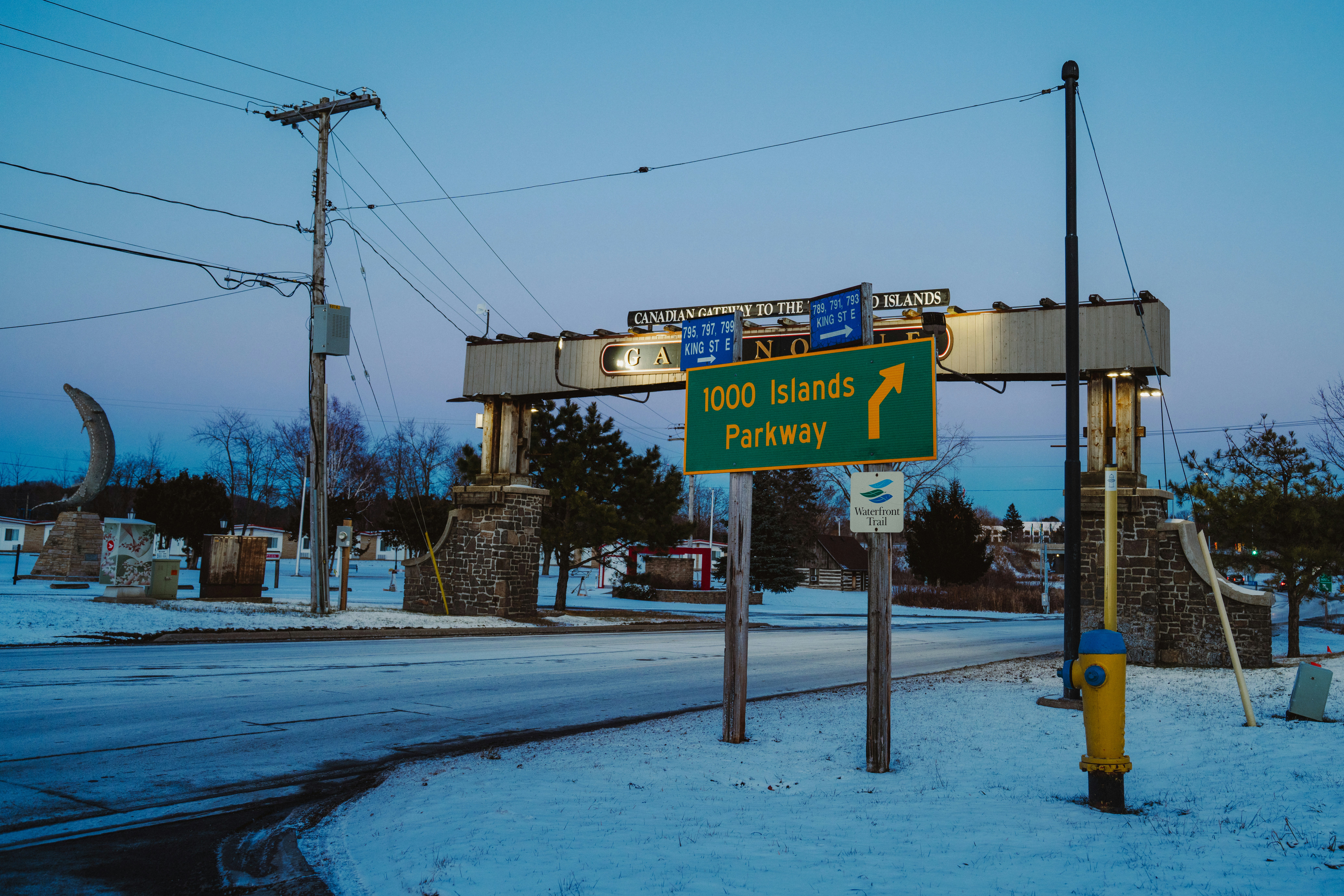 Snow-dusted road leading to a parkway entrance under a twilight sky.