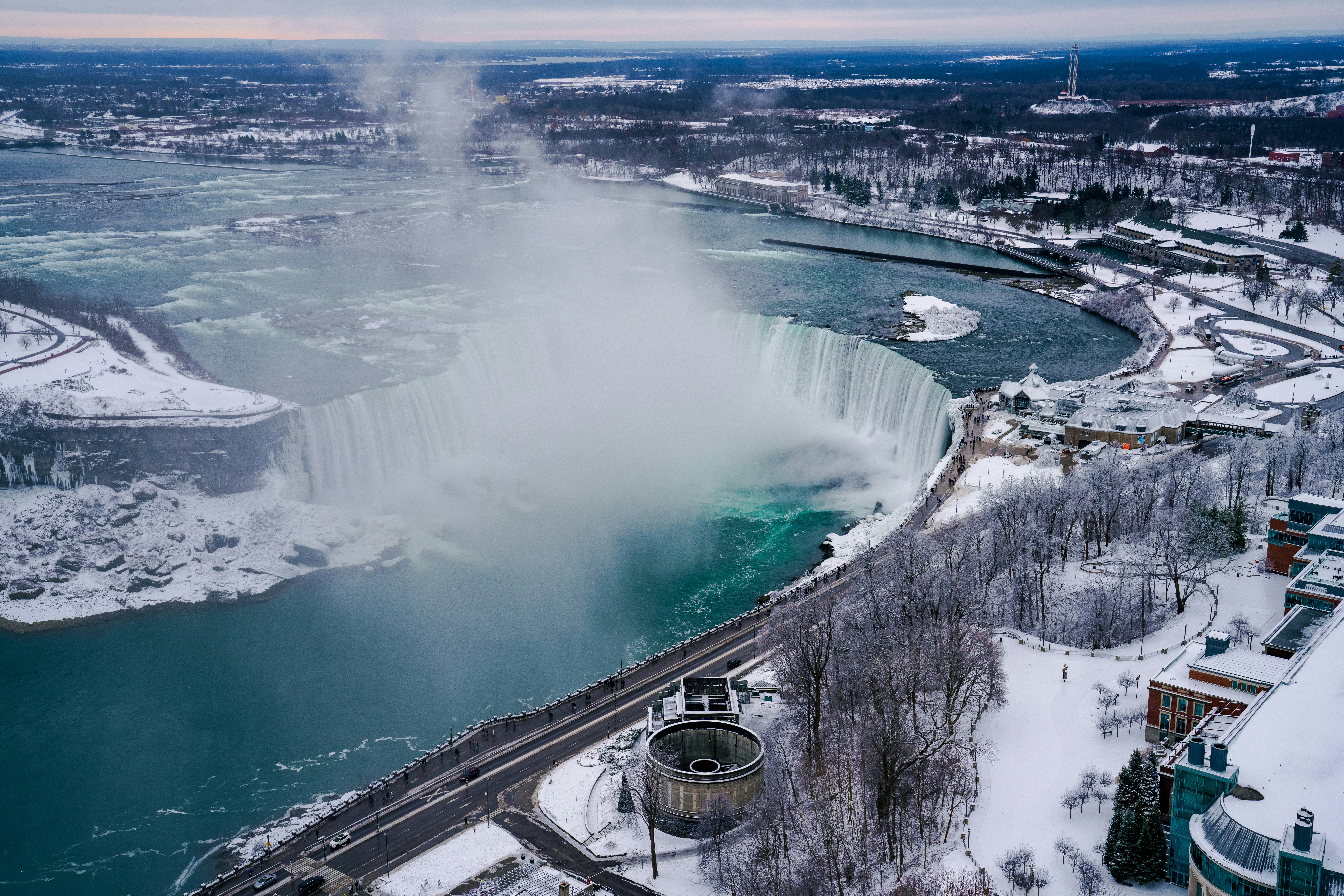 Aerial view of Niagara Falls shrouded in mist, surrounded by snow-covered landscapes and icy waters.