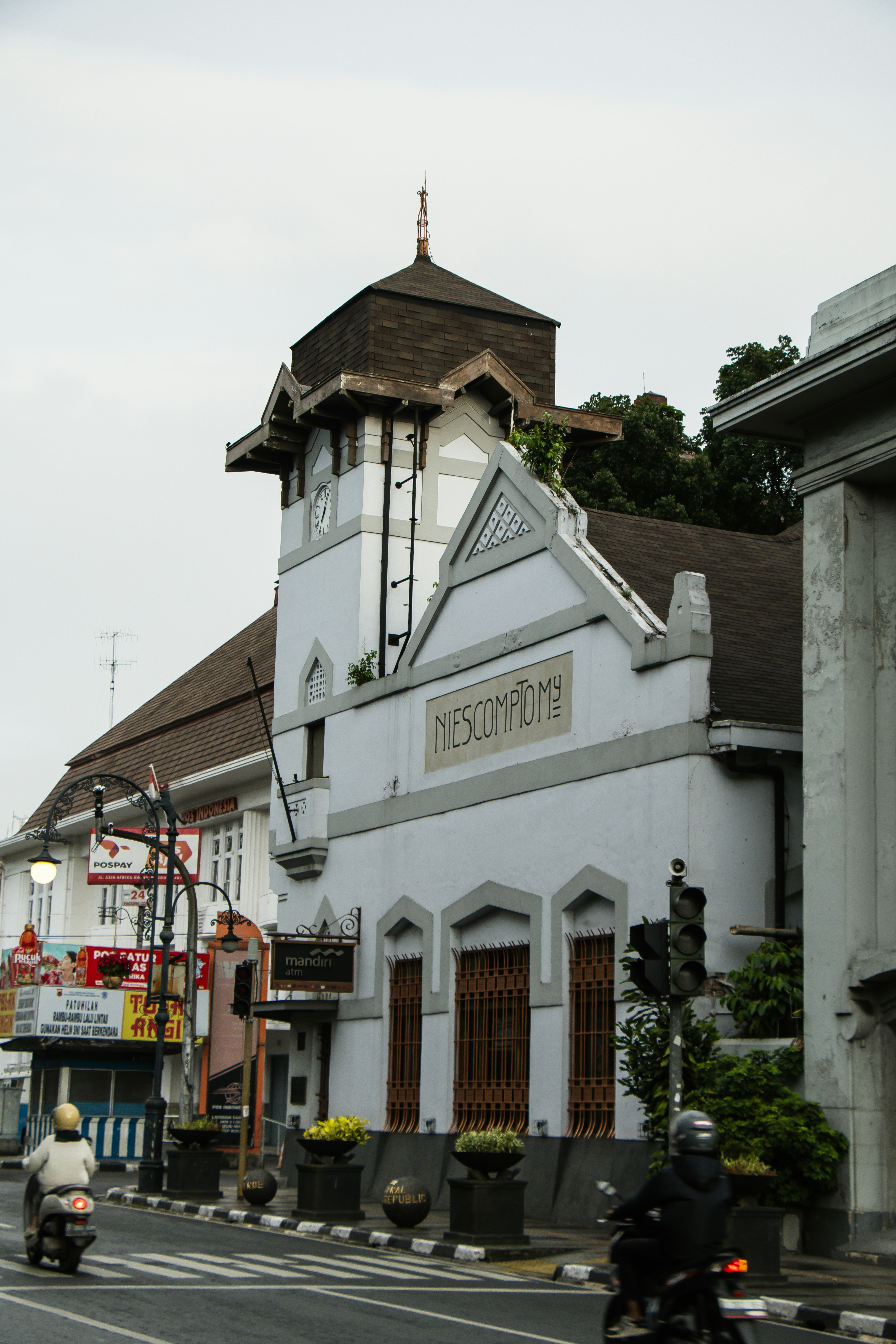 Historic building featuring intricate architectural details and a prominent clock tower, set against a bustling street scene. The structure reflects a blend of cultural influences.