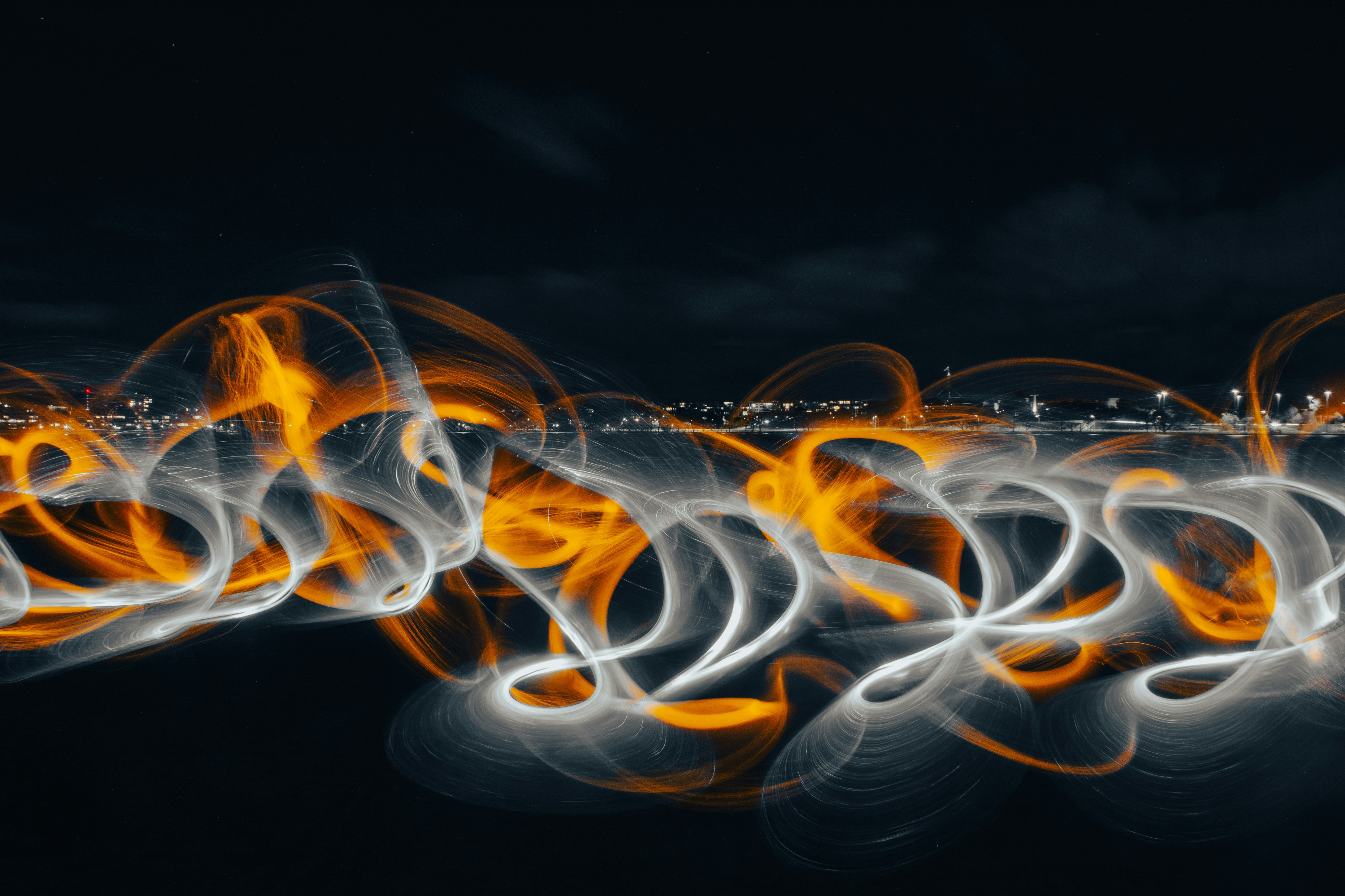 Abstract light trails in vibrant orange and white swirl against a dark backdrop, creating a dynamic visual rhythm.