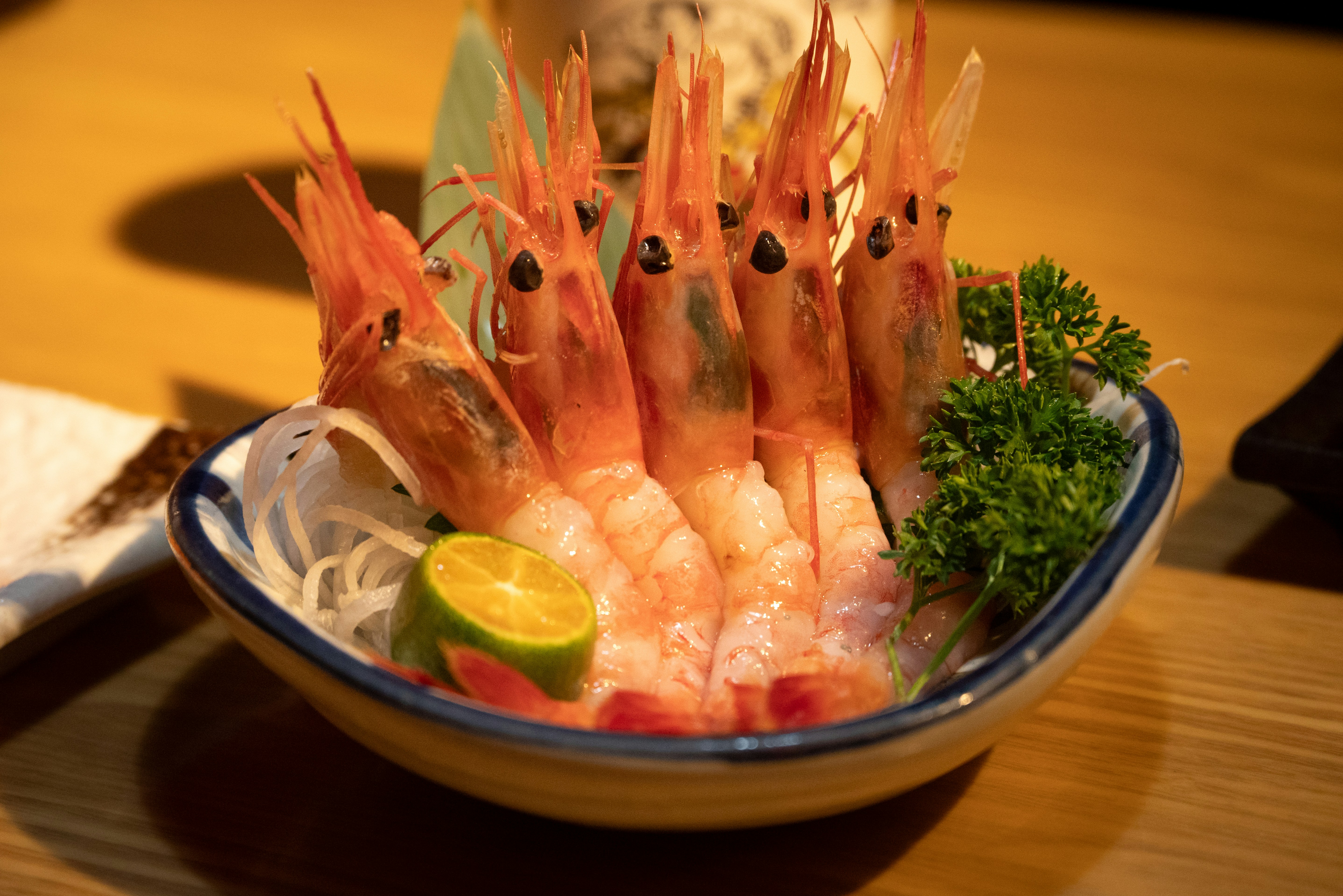 A dish of fresh prawns artfully arranged with lime and greens on a ceramic plate.