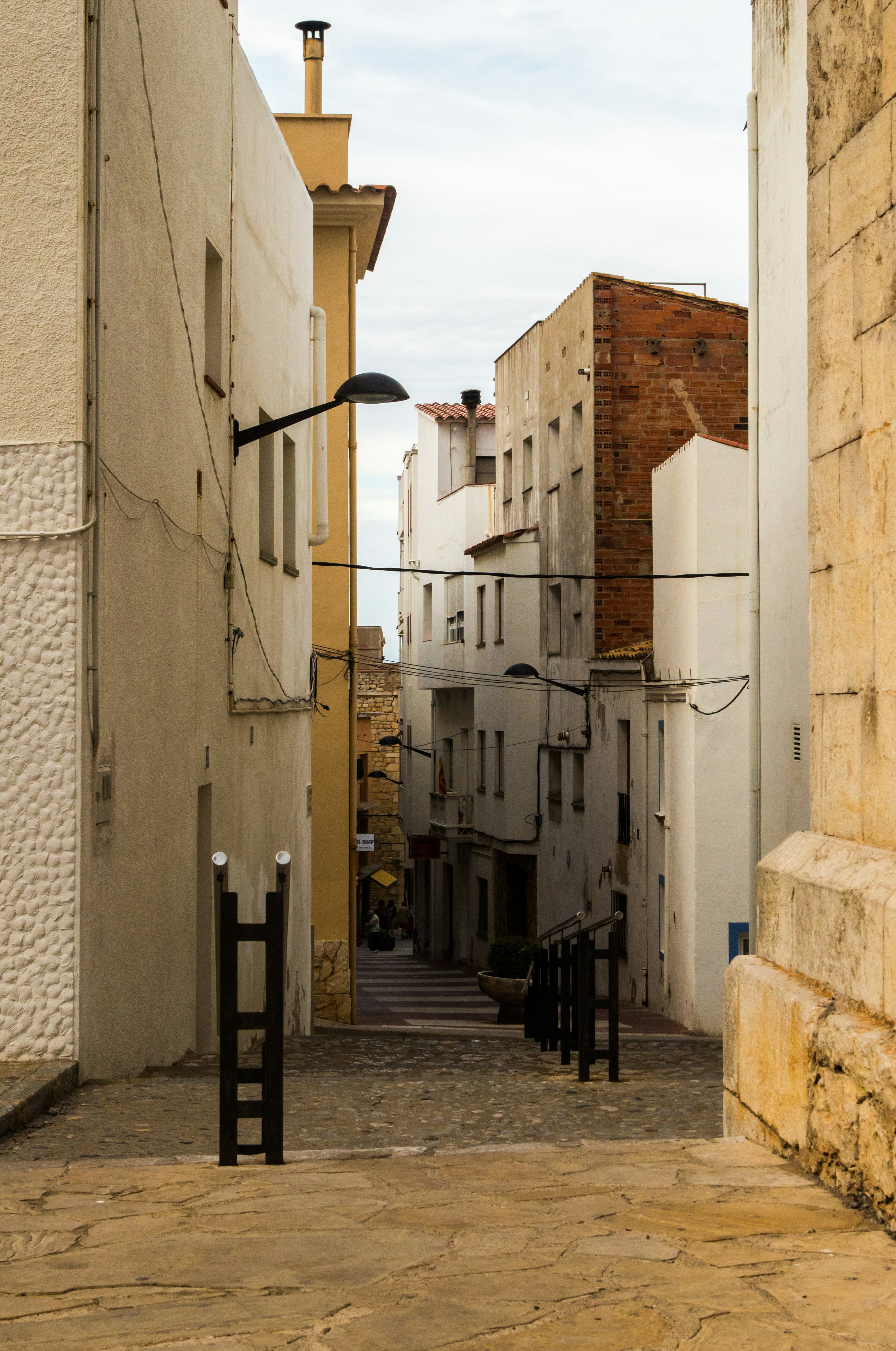 Narrow stone-paved street flanked by whitewashed buildings under a soft sky.