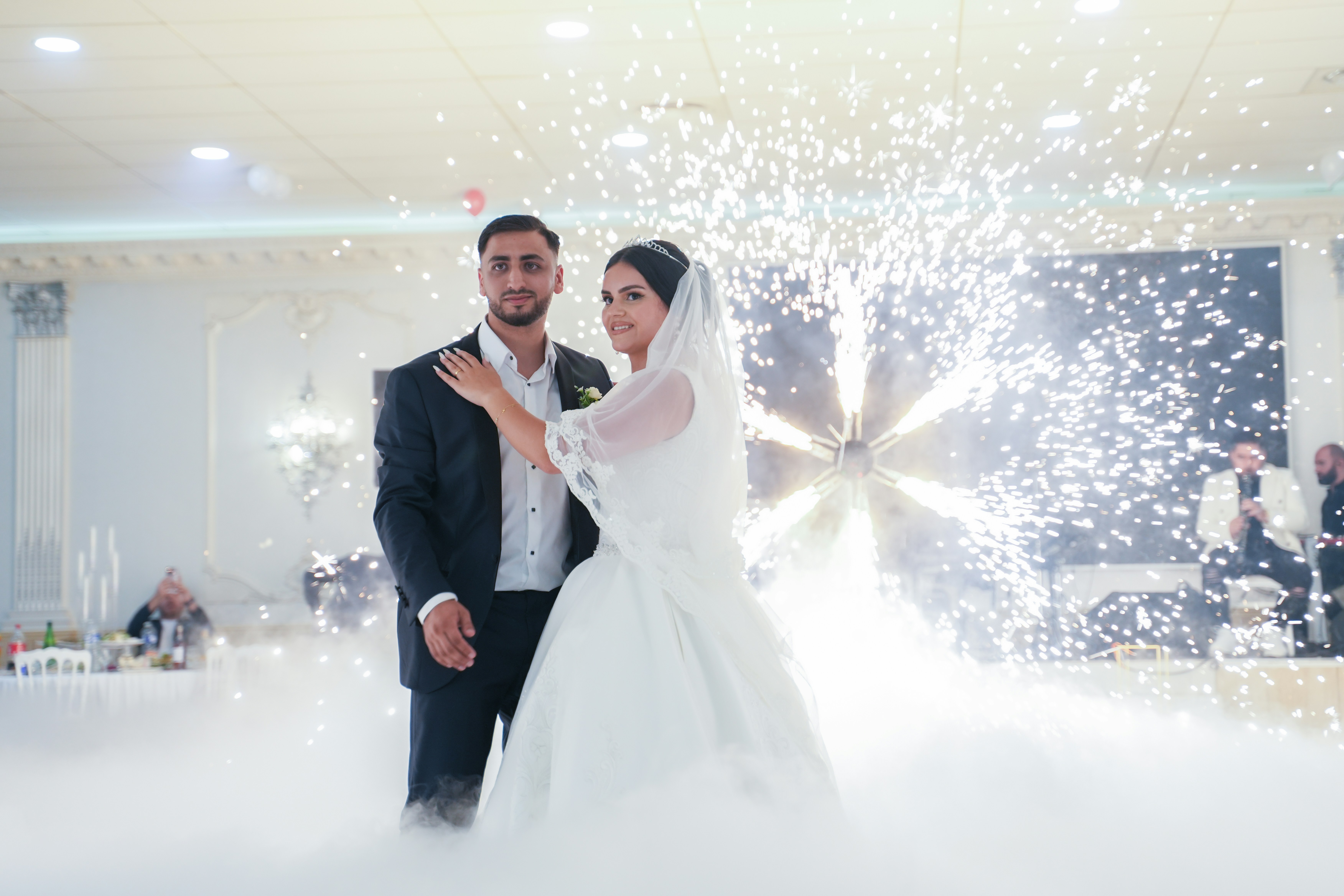 Bride and groom share a moment on the dance floor, surrounded by fog and sparkling lights. The atmosphere exudes joy and celebration.