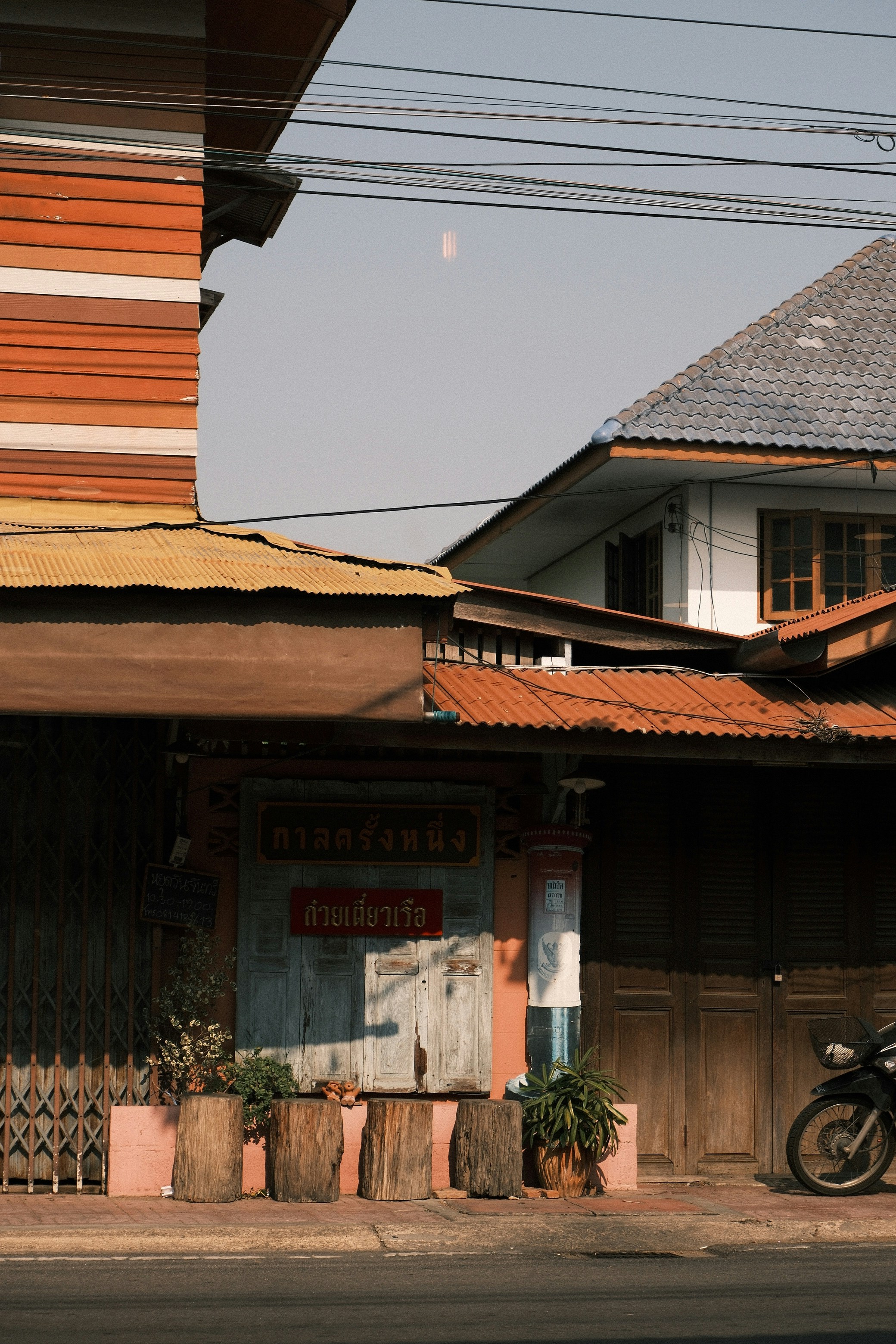 Sunlit Thai streetfronts beneath layered roofs and a parked motorcycle