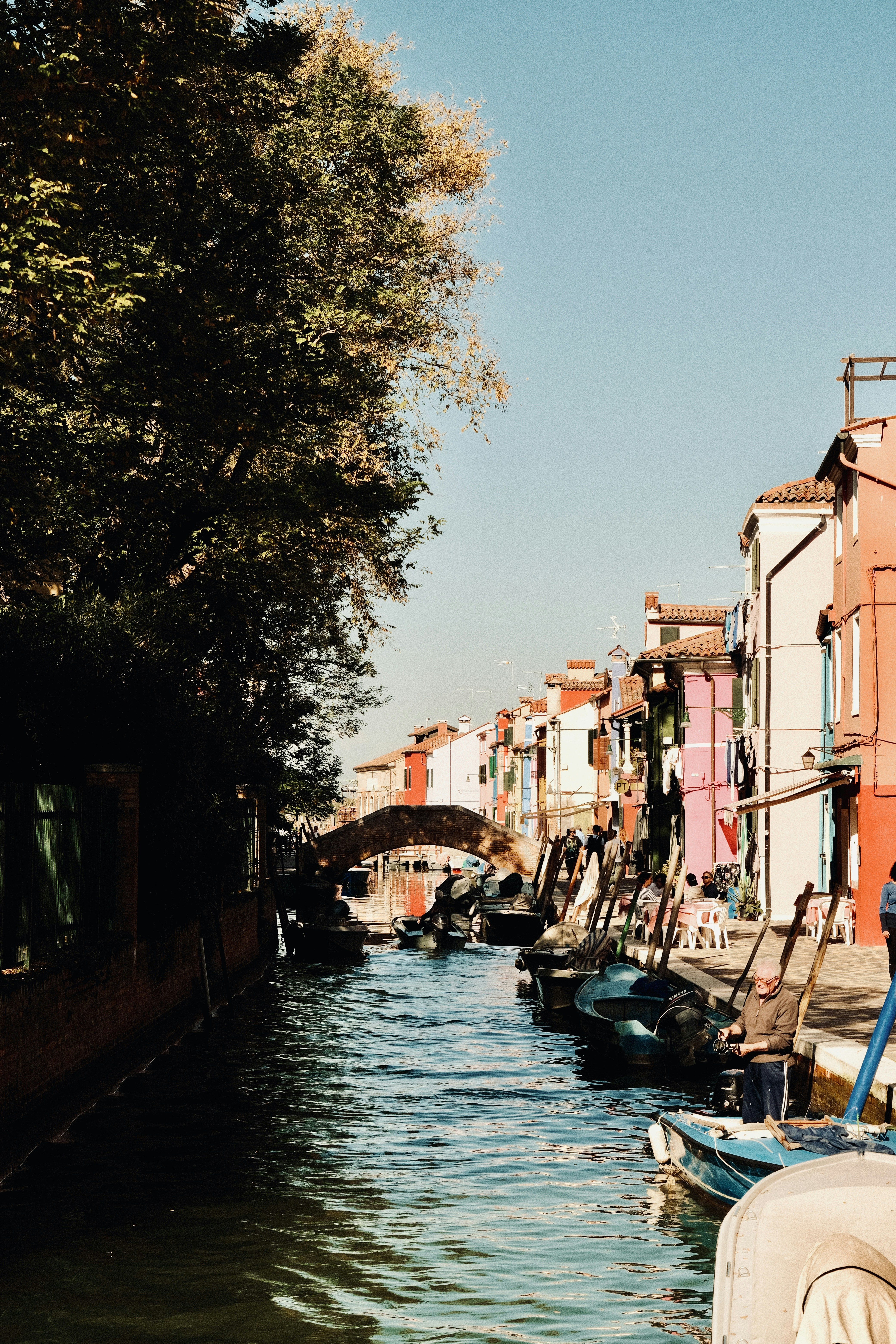 Colorful houses line a canal in Burano, Italy, with boats gently moored along its edges.