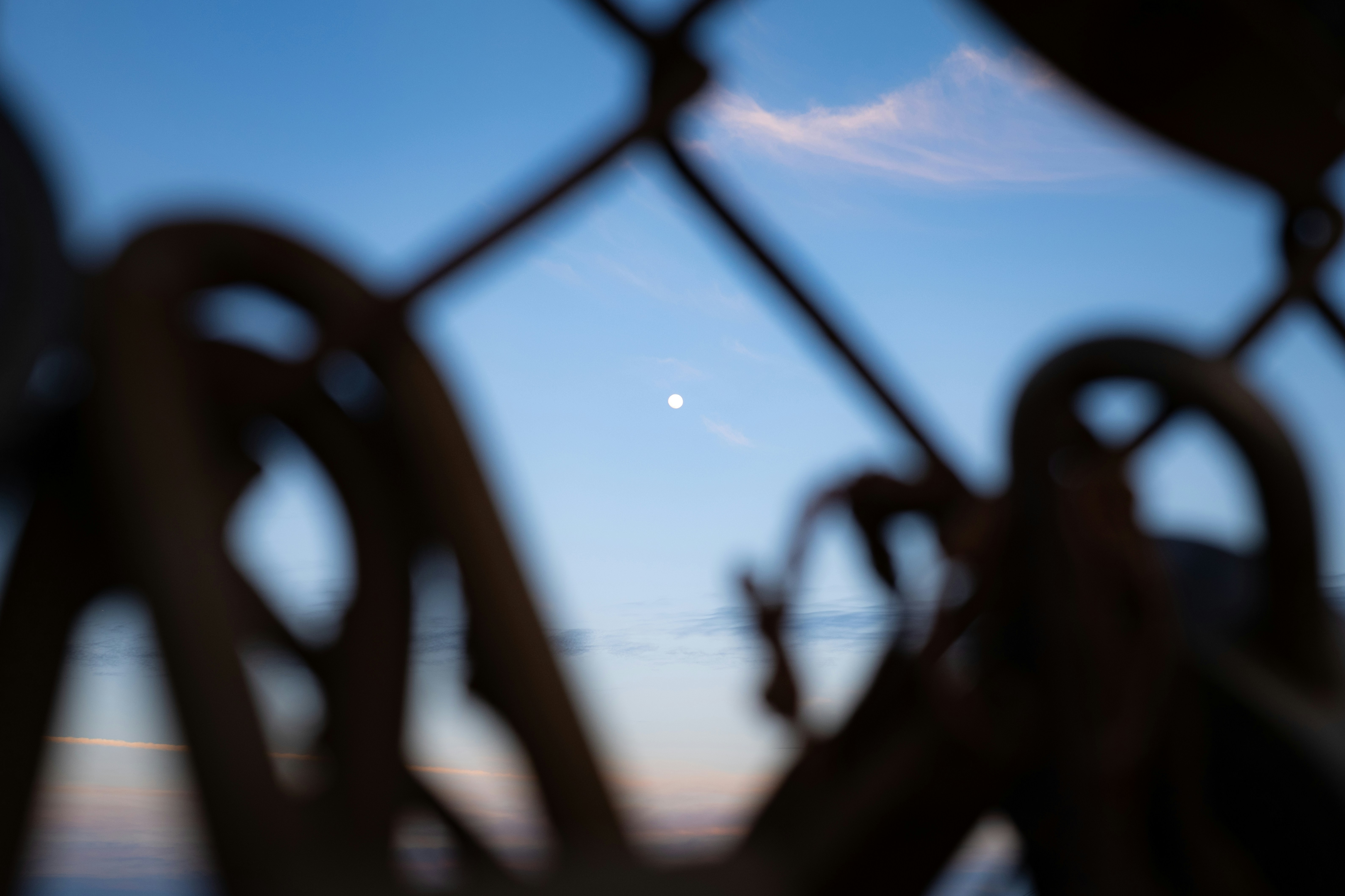 Moonlit Mesh: Moon seen through a blurred chain-link foreground