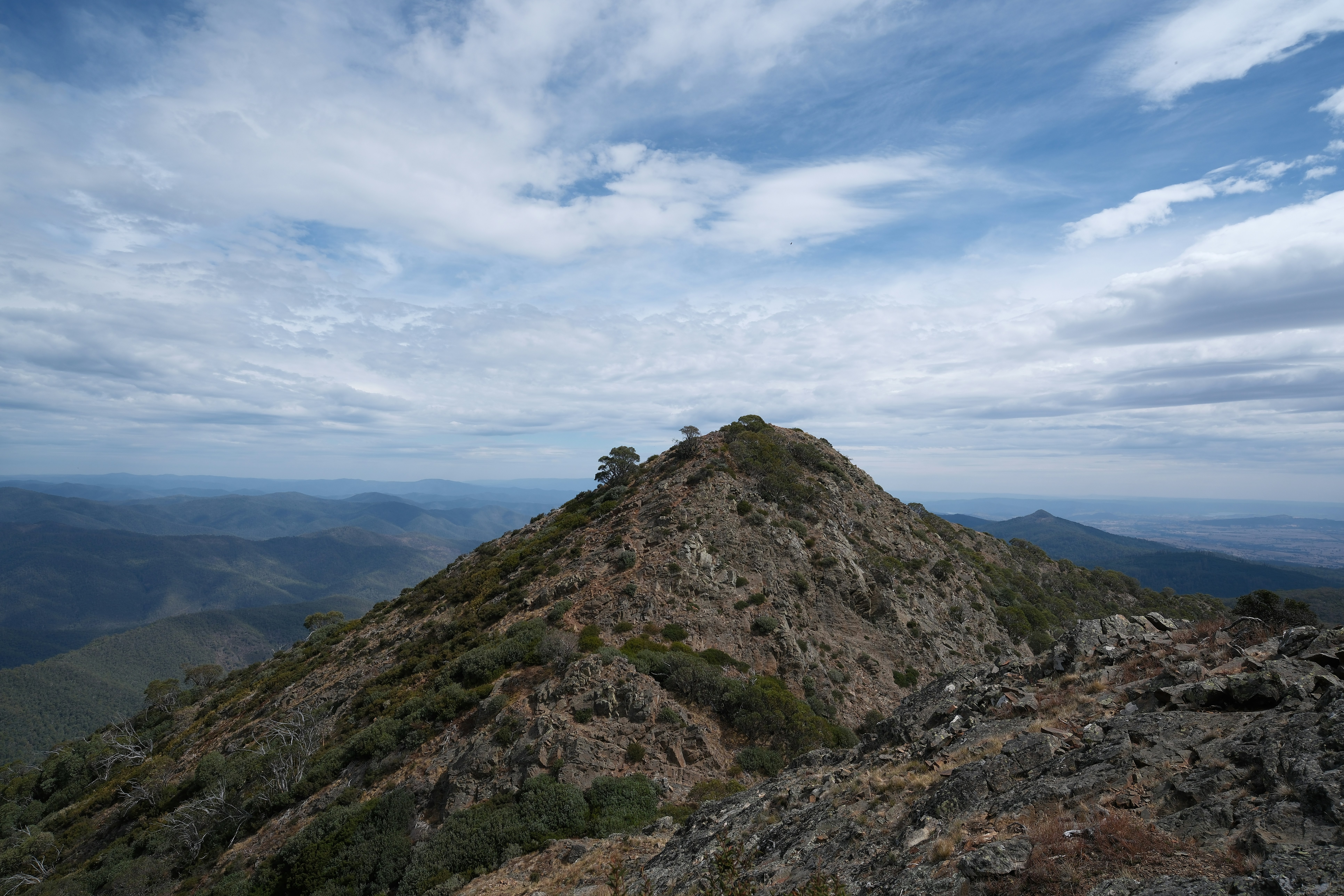 Rocky mountain peak with sparse vegetation under a vast, cloud-filled sky.