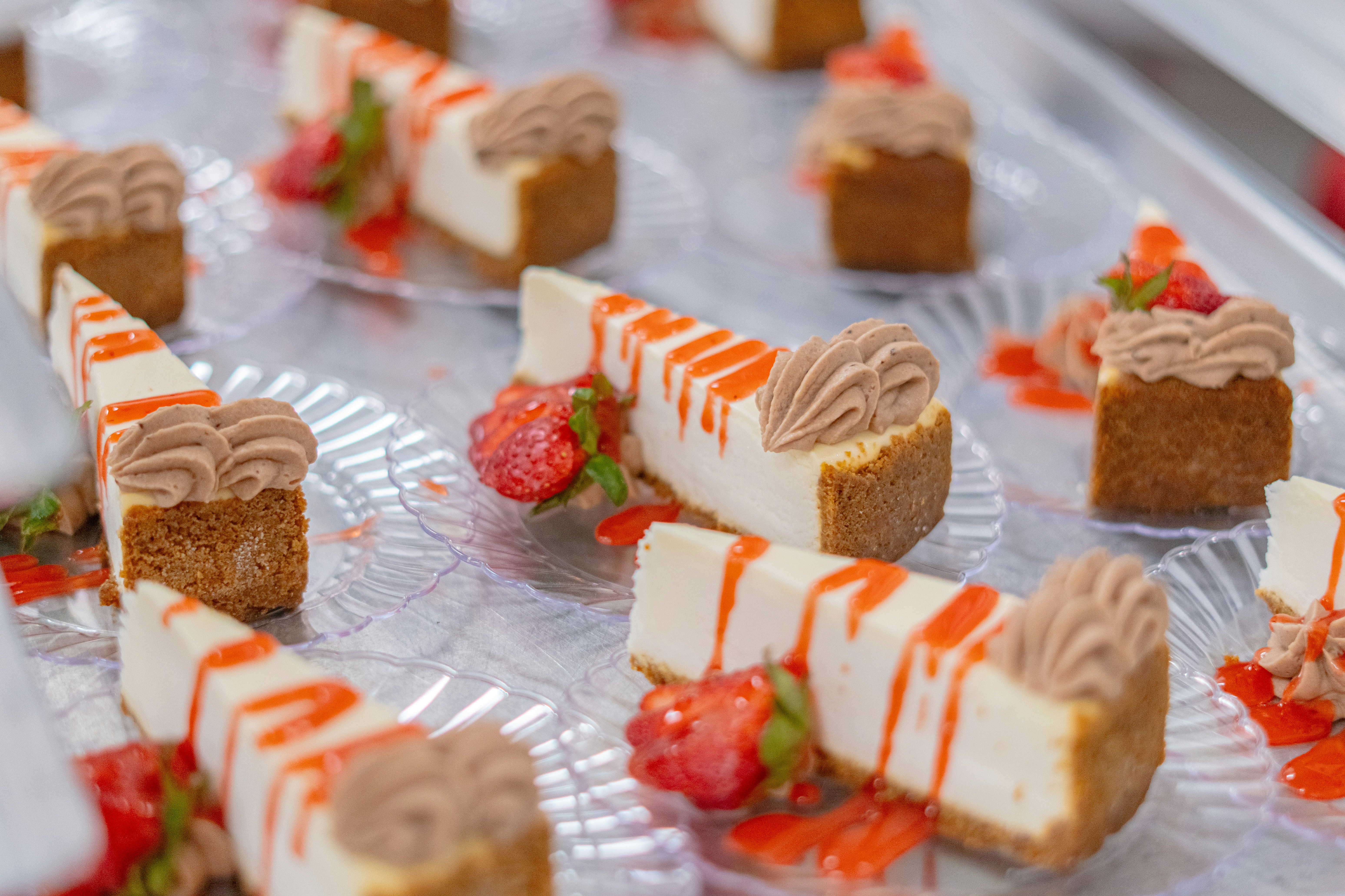 Slices of cheesecake adorned with whipped cream and strawberries on a decorative platter.