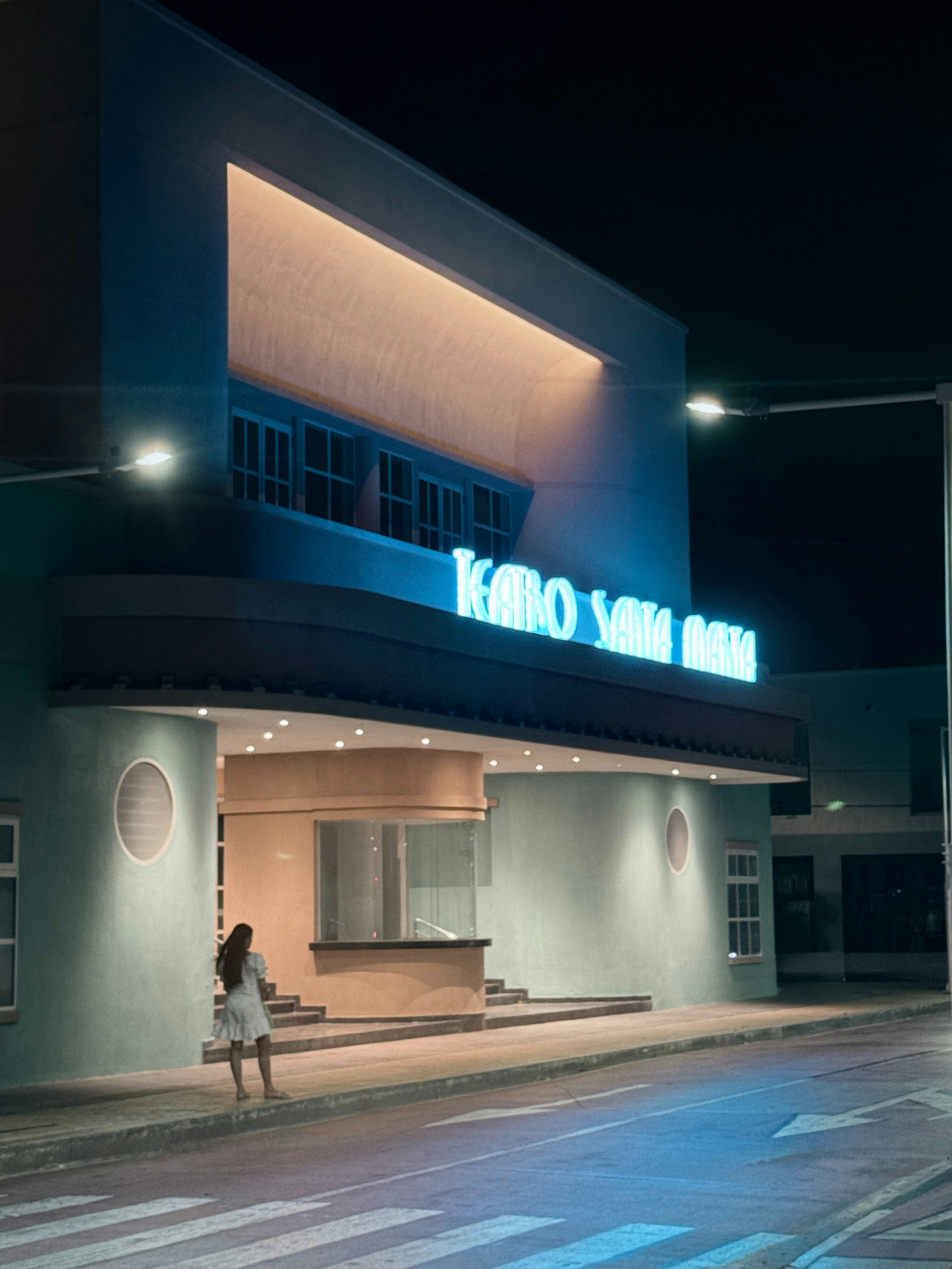 Woman walking past an illuminated art deco theater at night.