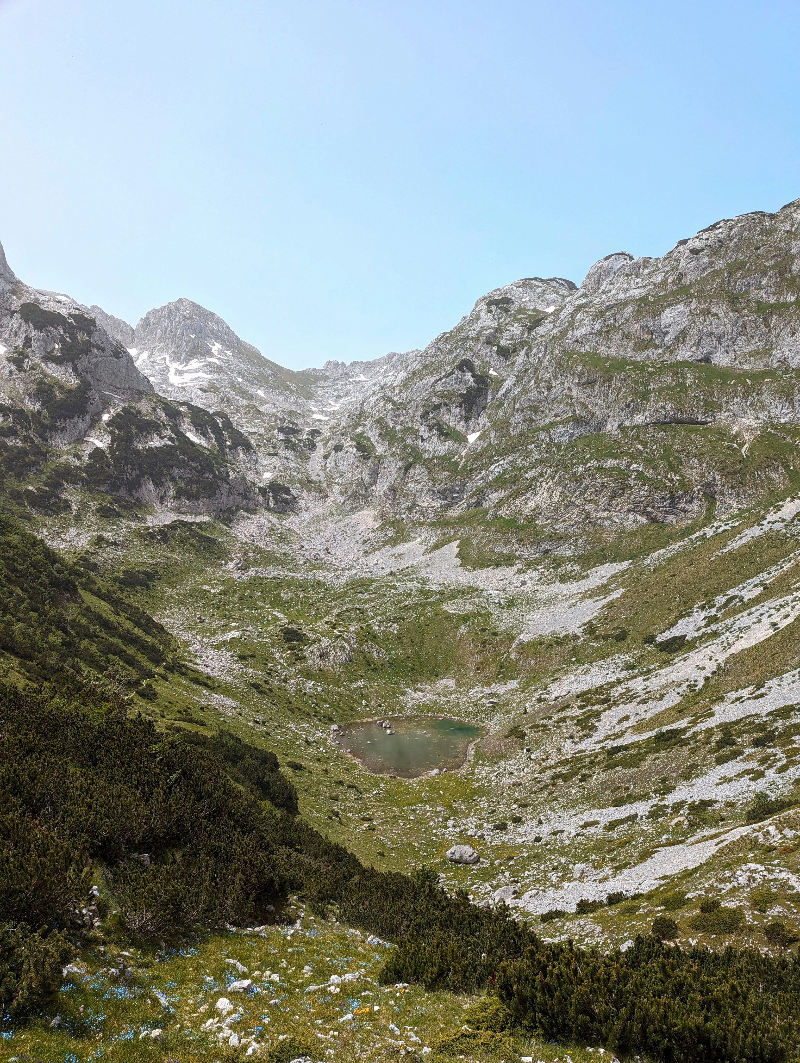 Mountain valley with rugged peaks and a small lake under clear blue skies.