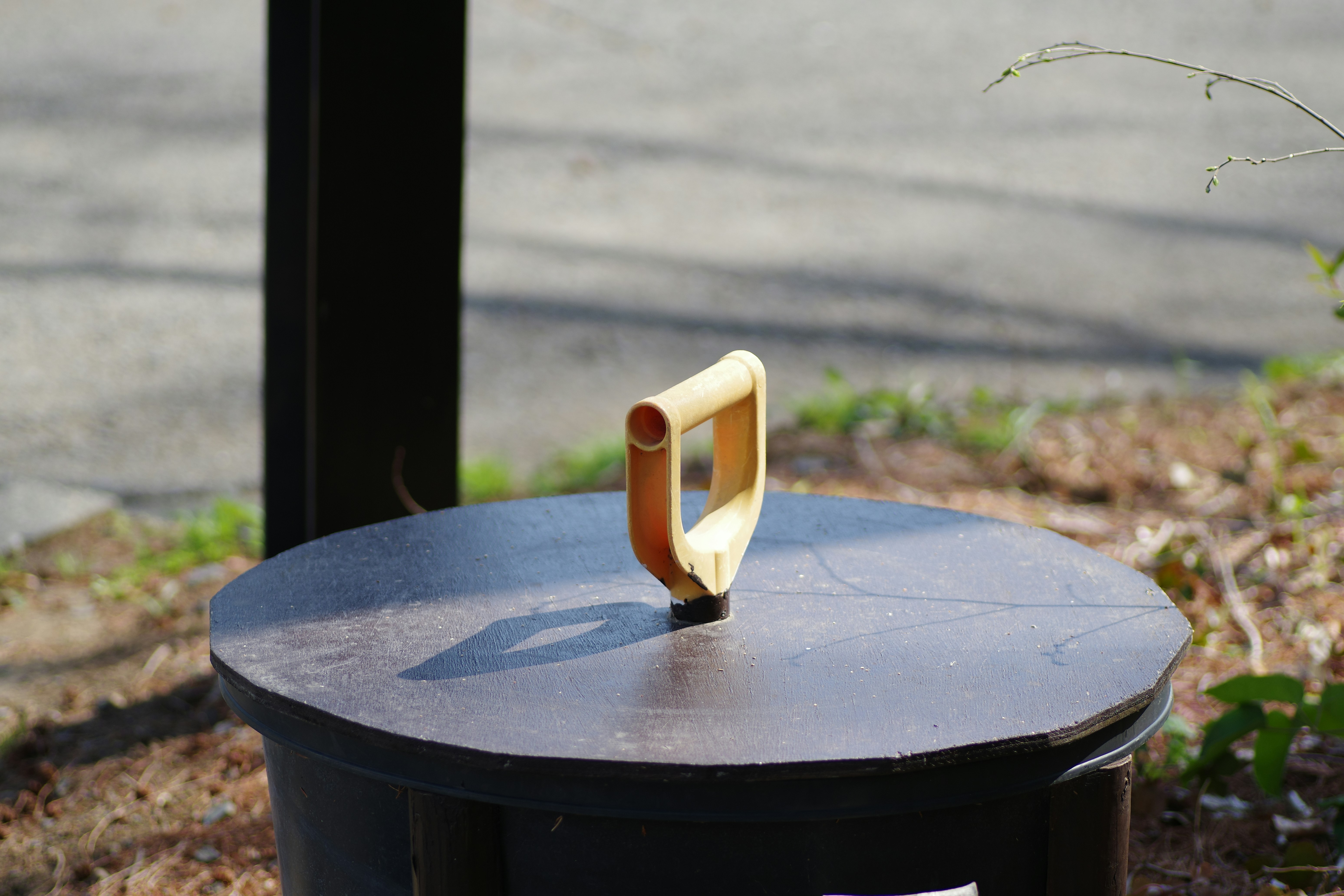 Lone Yellow Handle on a Weathered Blue Canister Lid in Quiet Urban Light