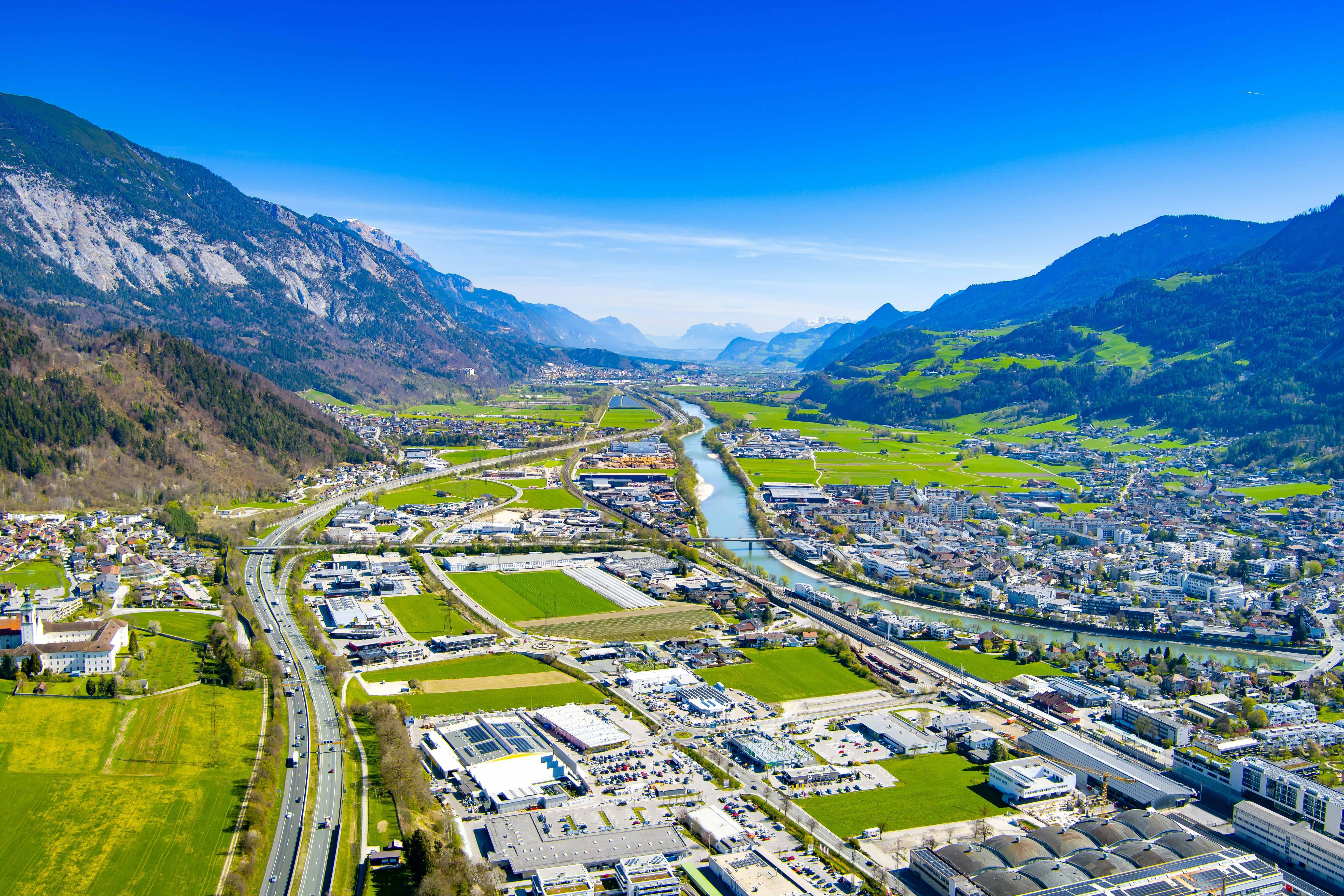 Spring in Schwaz, Südtirol – where vibrant green meadows contrast with snow-capped peaks under a bright blue sky. A breathtaking alpine landscape.