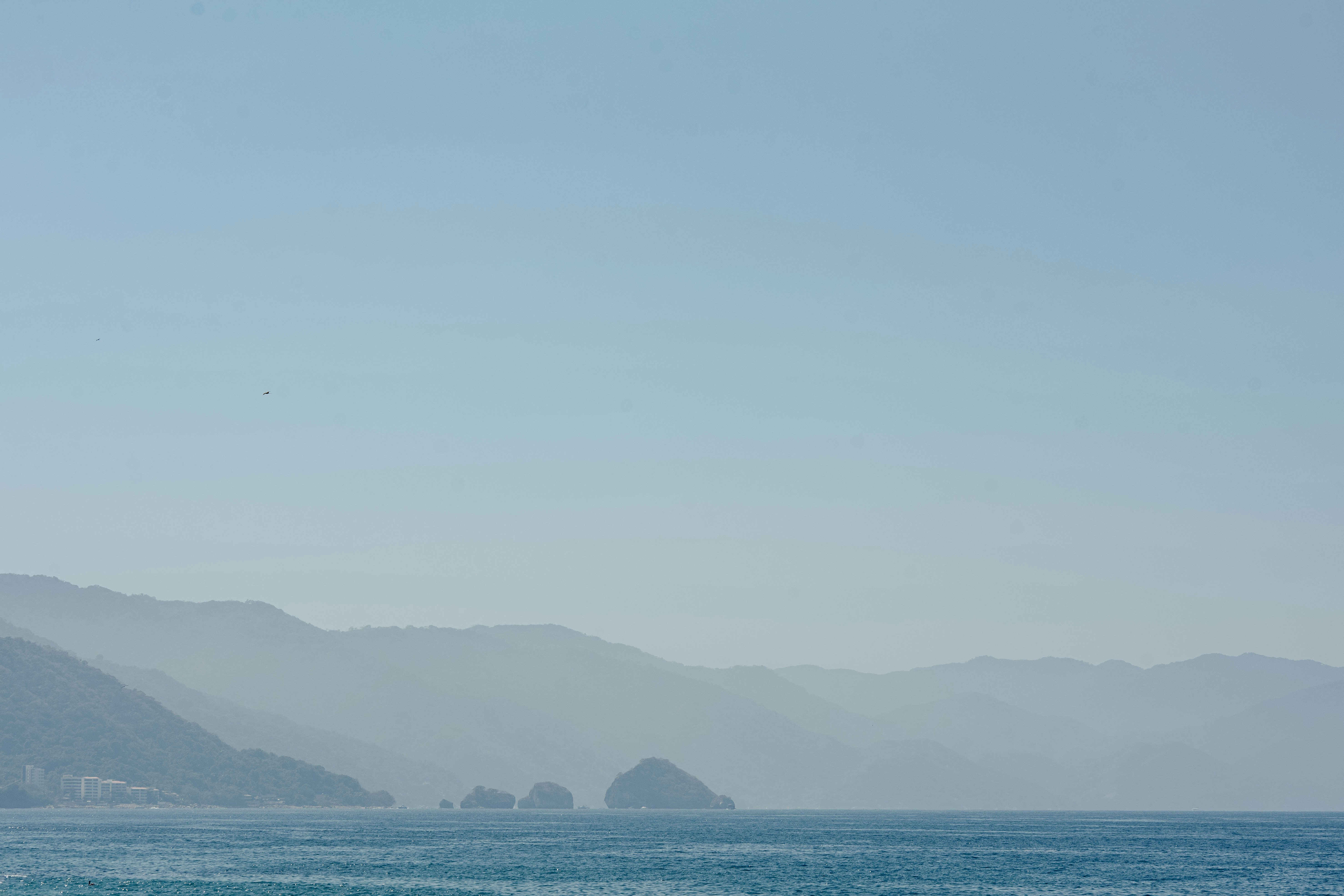 Calm ocean waters with distant layered mountain silhouettes under a clear blue sky.