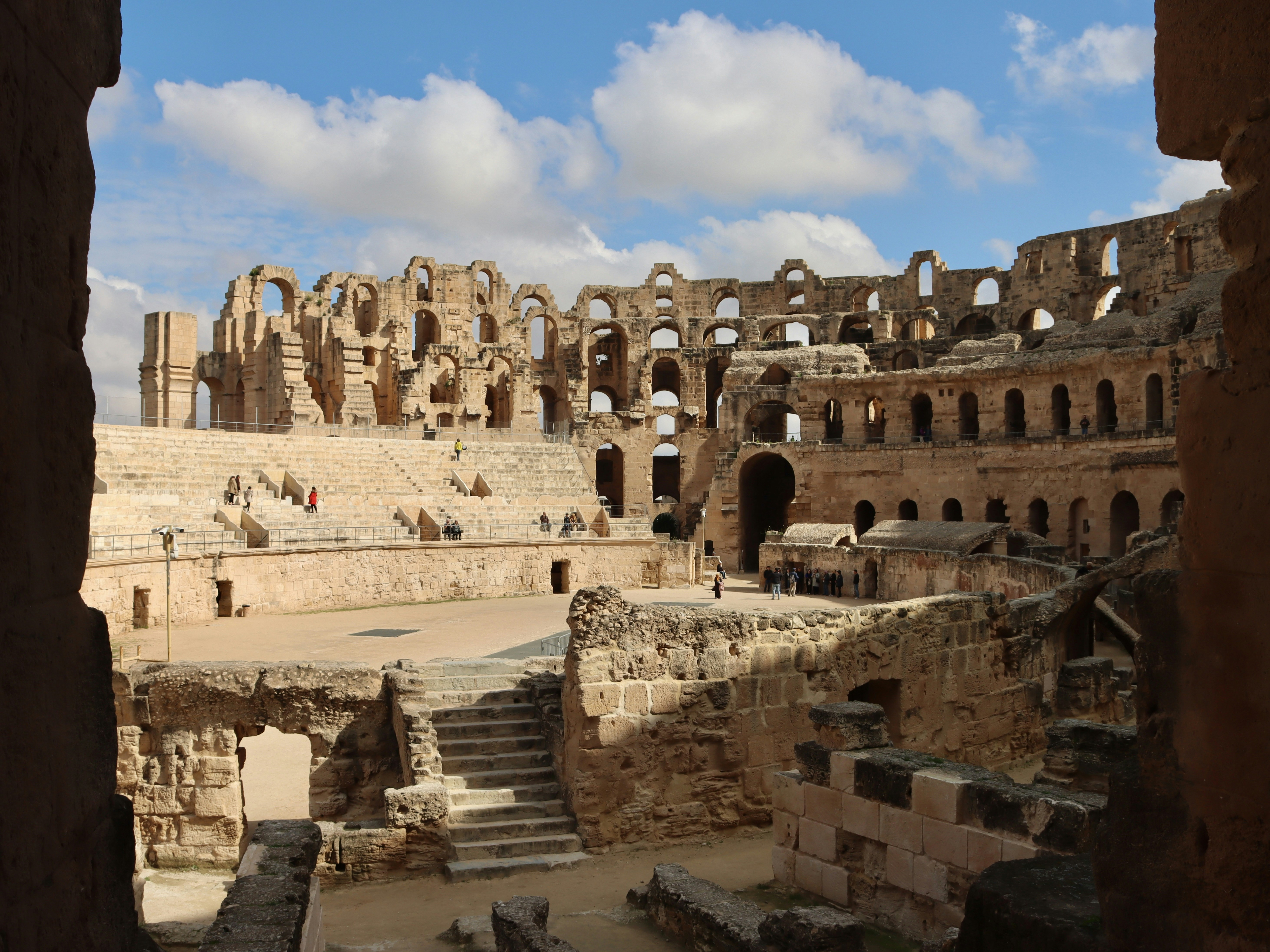 Roman amphitheater with stone arches under a partly cloudy sky.