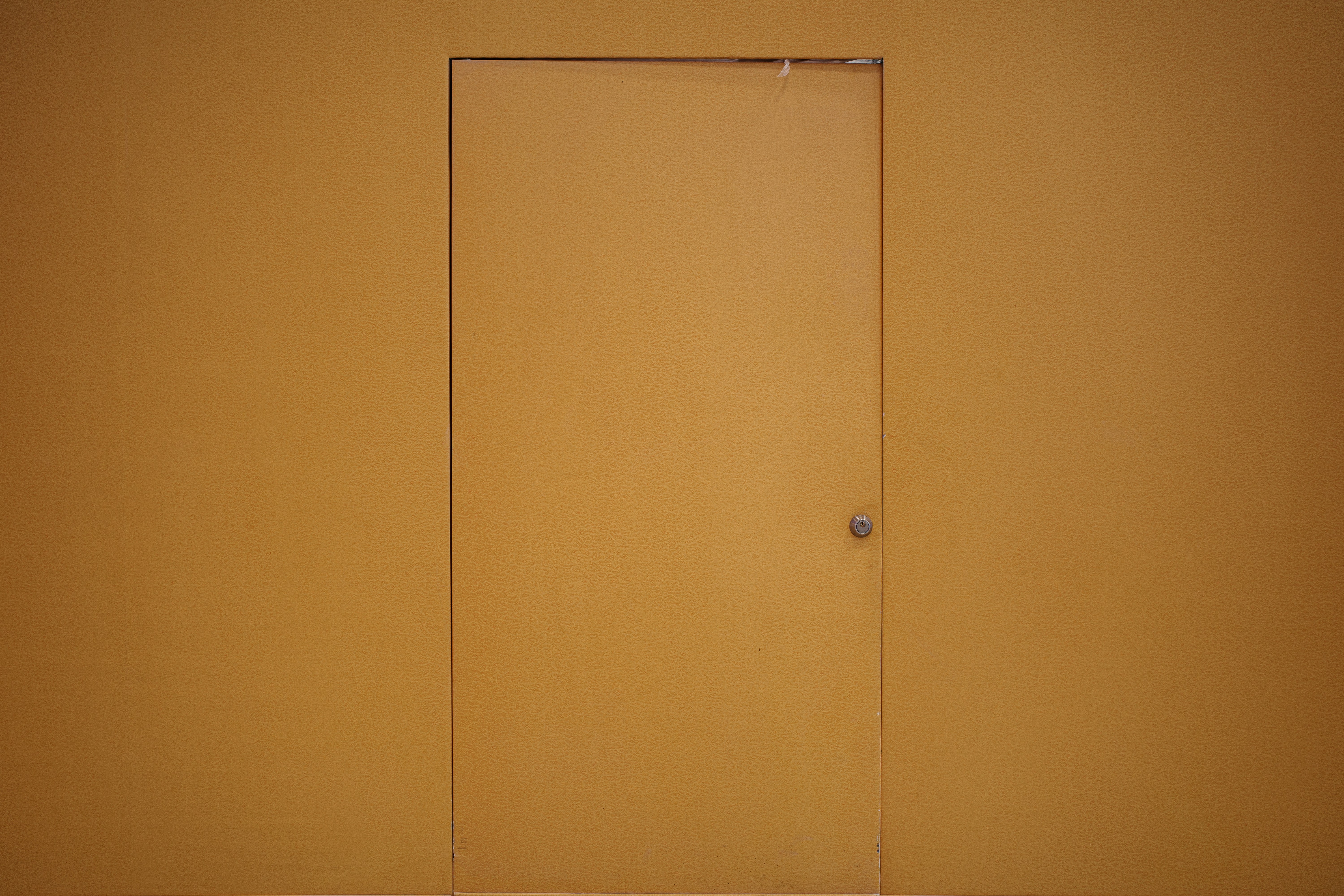 A solitary amber door set in a sun-warmed, flat wall, emphasizing pure geometry and subtle texture.
