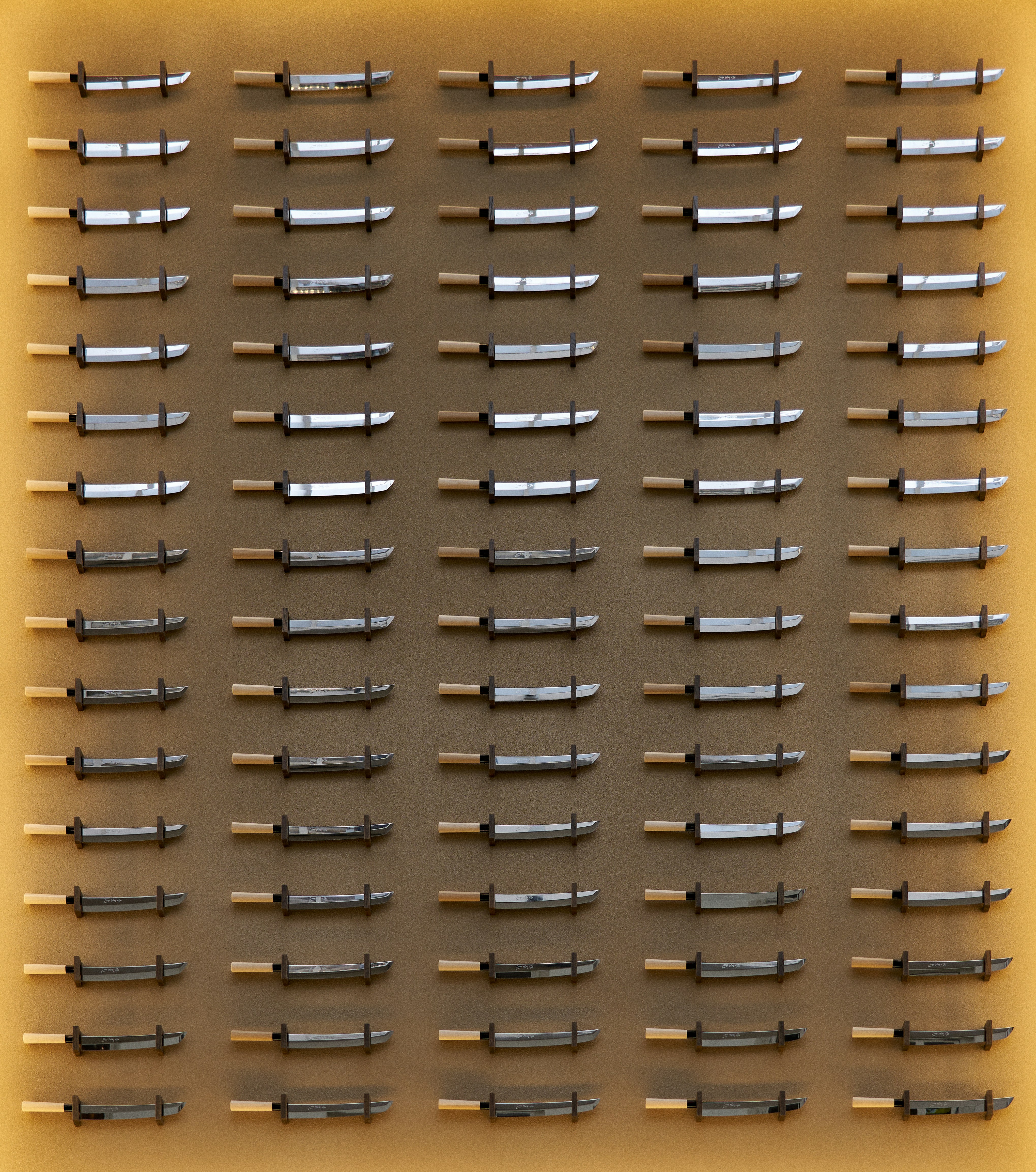 A meticulously arranged collection of knives displayed in a grid pattern, showcasing their varied designs and craftsmanship.