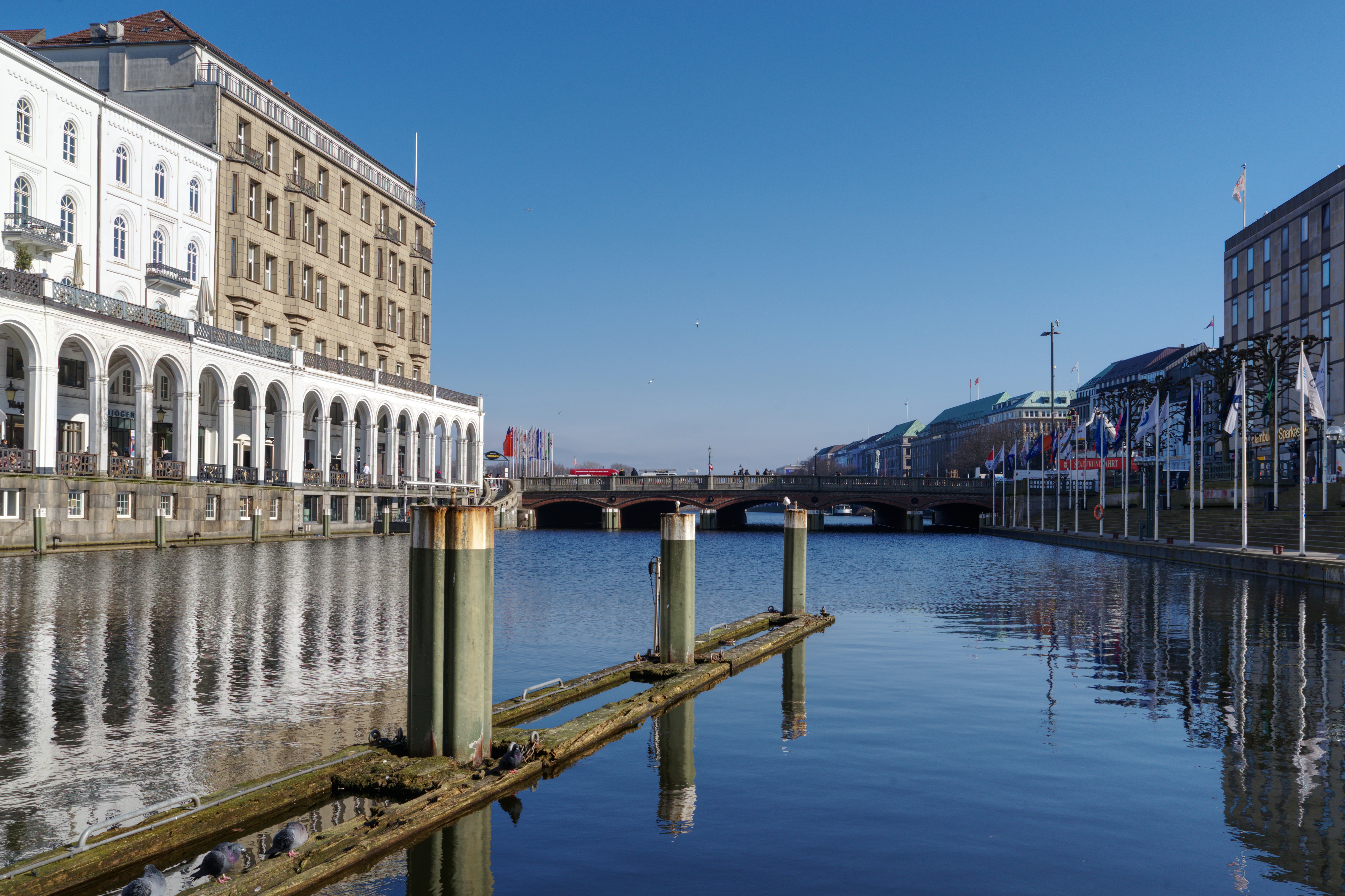 Canal flanked by historic buildings with clear reflections in the calm water under a bright blue sky.