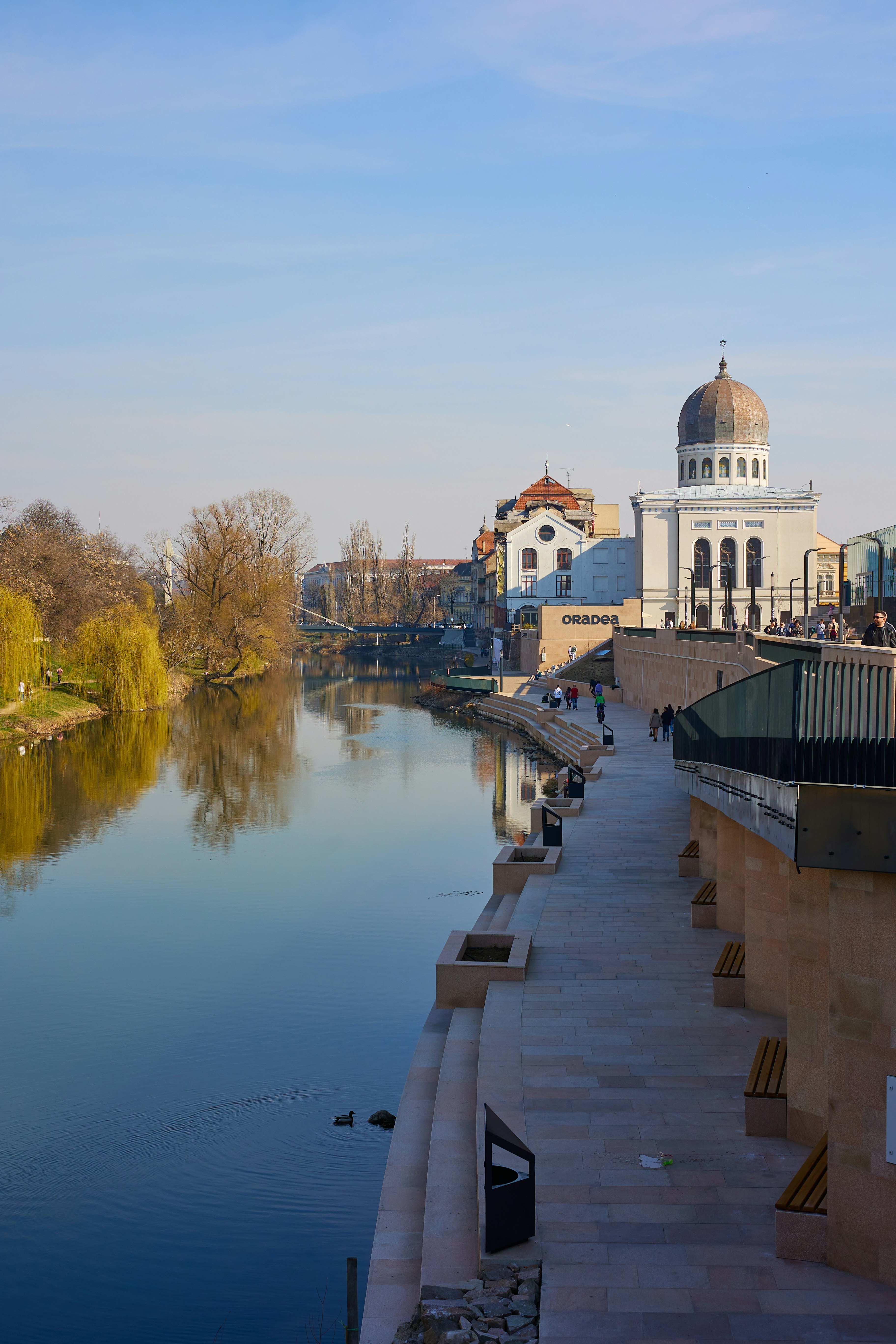 A river flows beside buildings under a blue sky. photo – Free Travel ...