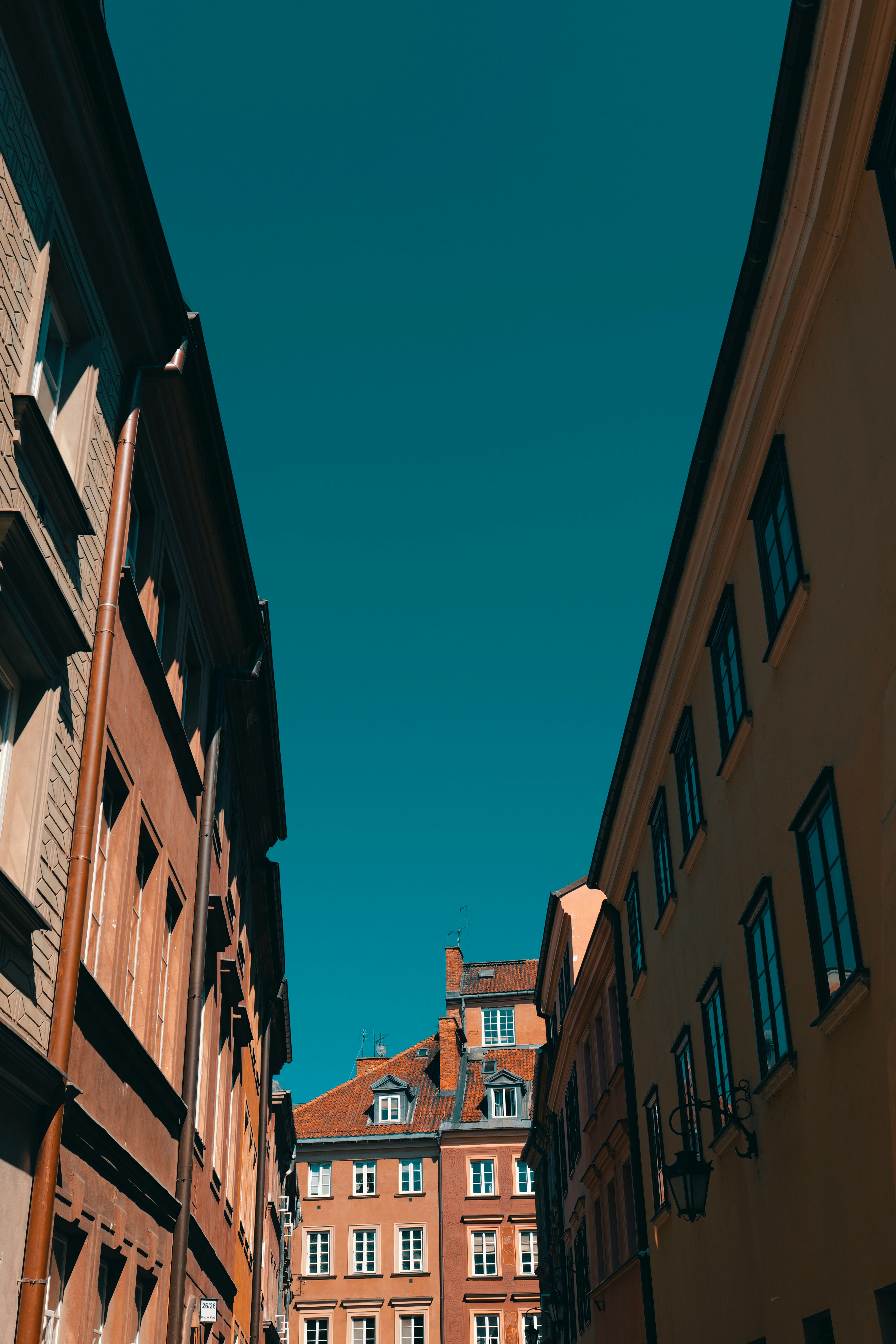 Narrow alleyway flanked by historic buildings, leading towards a clear blue sky. The architectural details create a striking perspective.