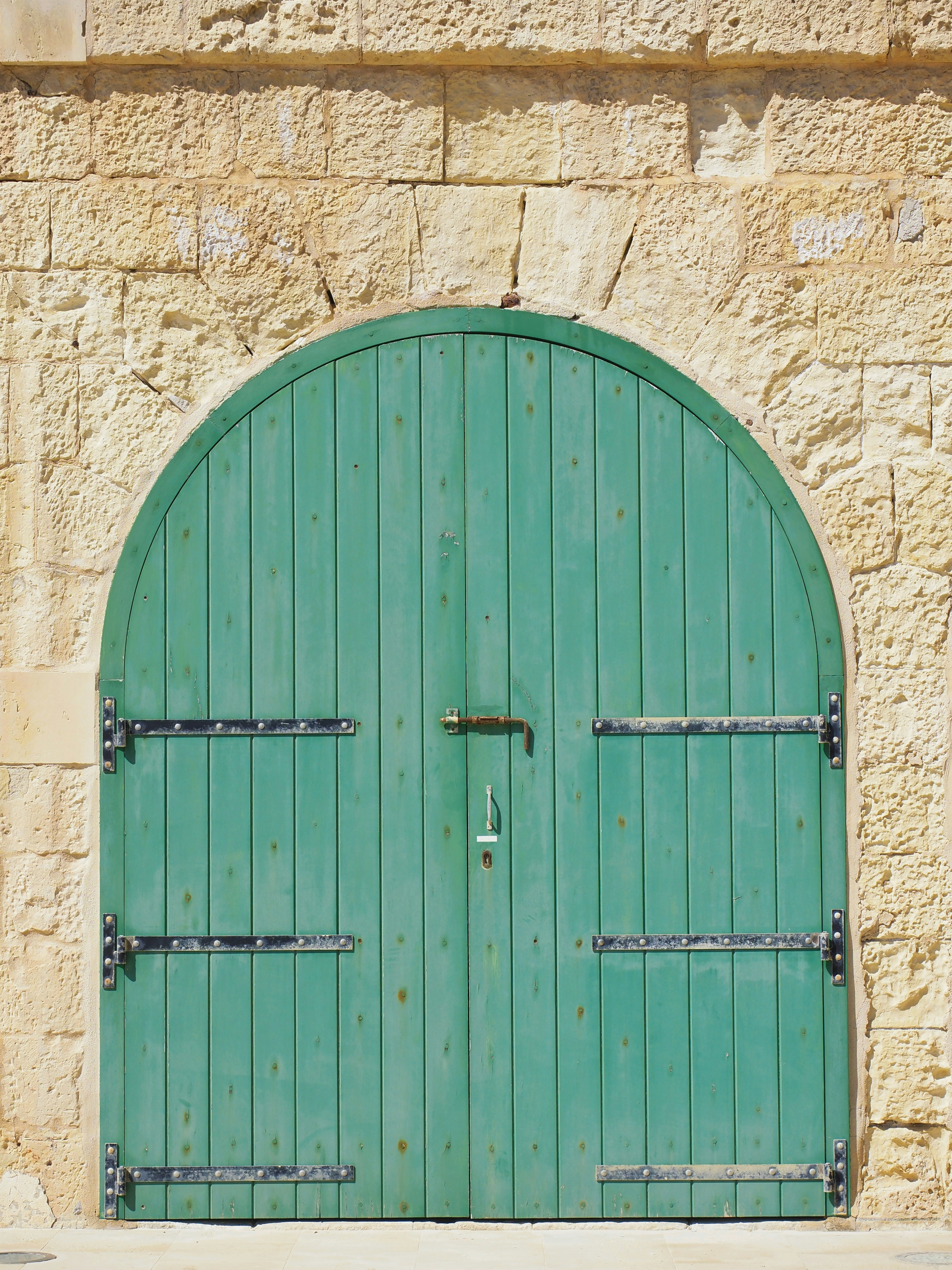 Arched green wooden door with metal fittings set against a weathered stone wall. The door's intricate details hint at a rich history.