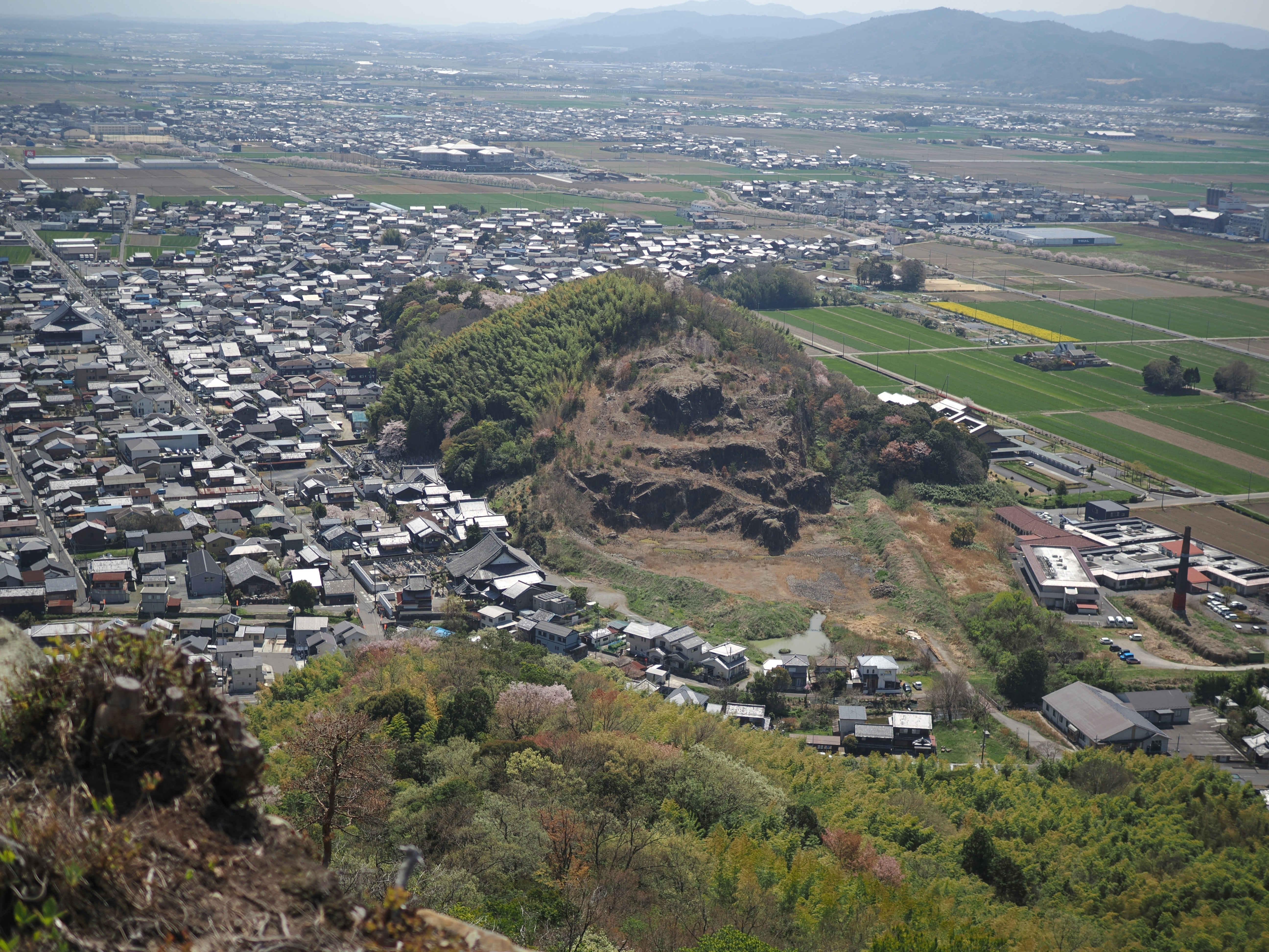 Aerial view showcasing a rugged hill surrounded by a sprawling urban landscape, emphasizing the contrast between natural and built environments.