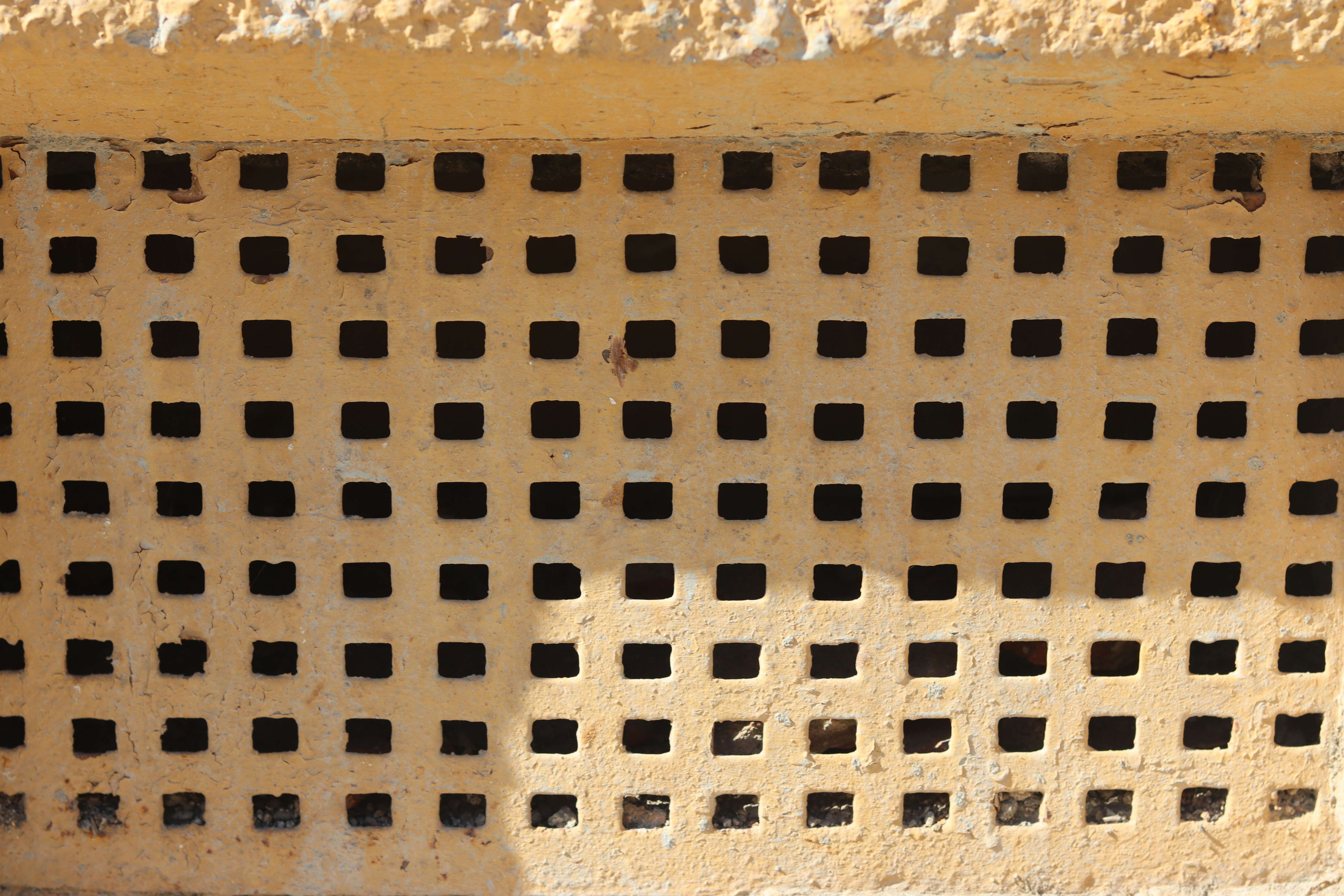 Sunlit Square Grid: a warm close-up of a perforated panel