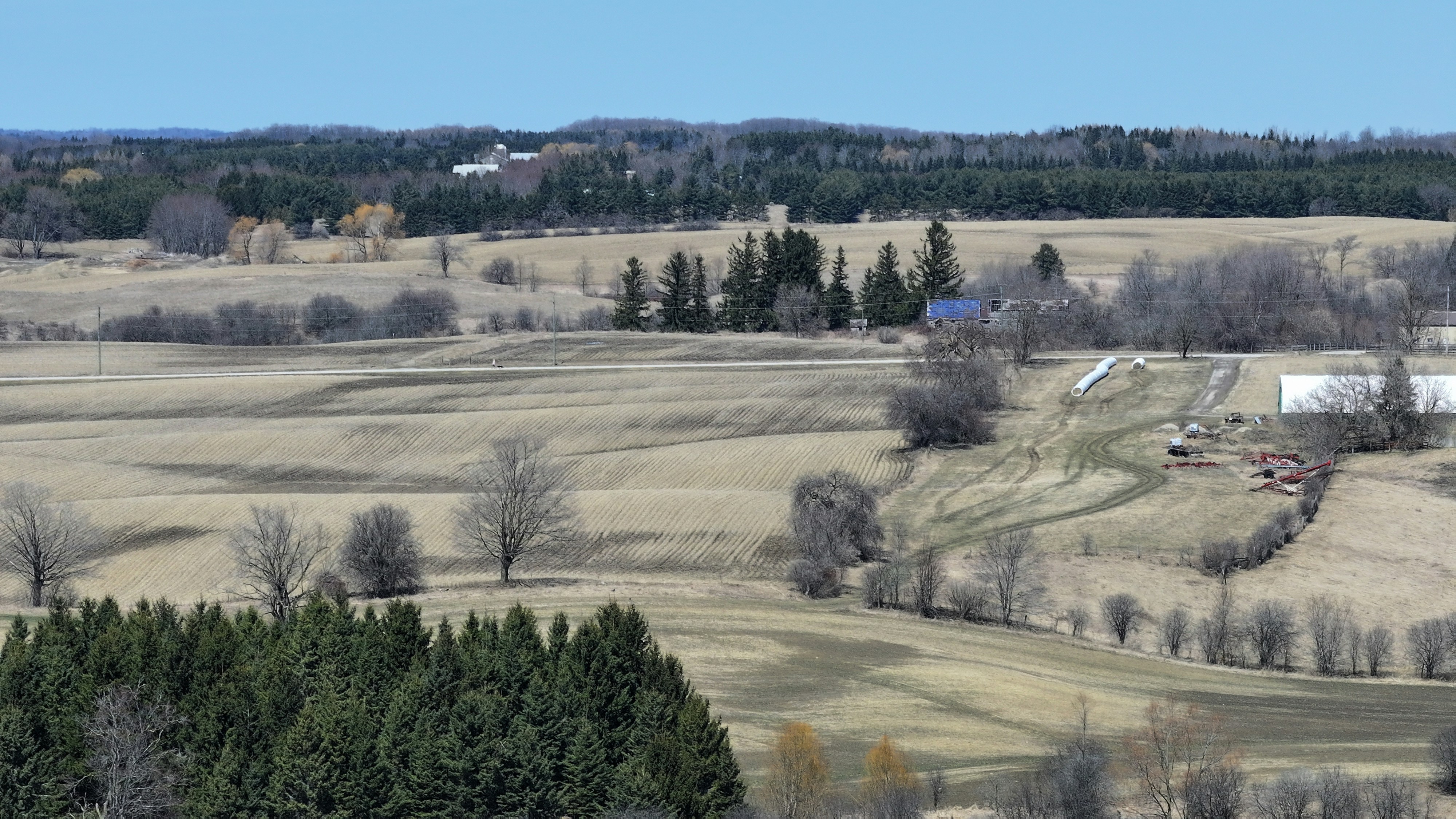 Expansive rural landscape showcasing a blend of cultivated fields and patches of forest under a clear blue sky.