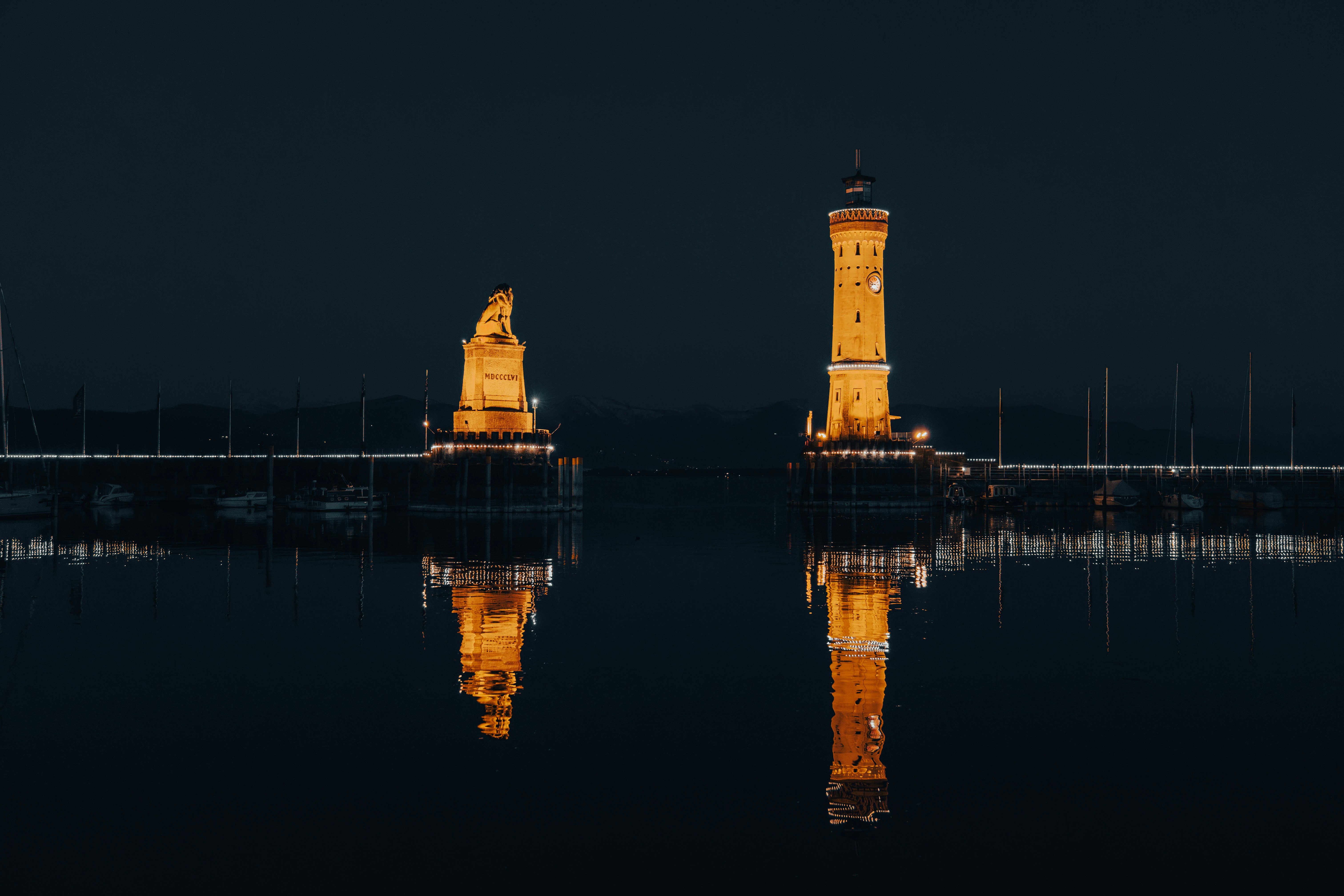 A lighthouse and statue reflect in still water at night. photo – Free ...