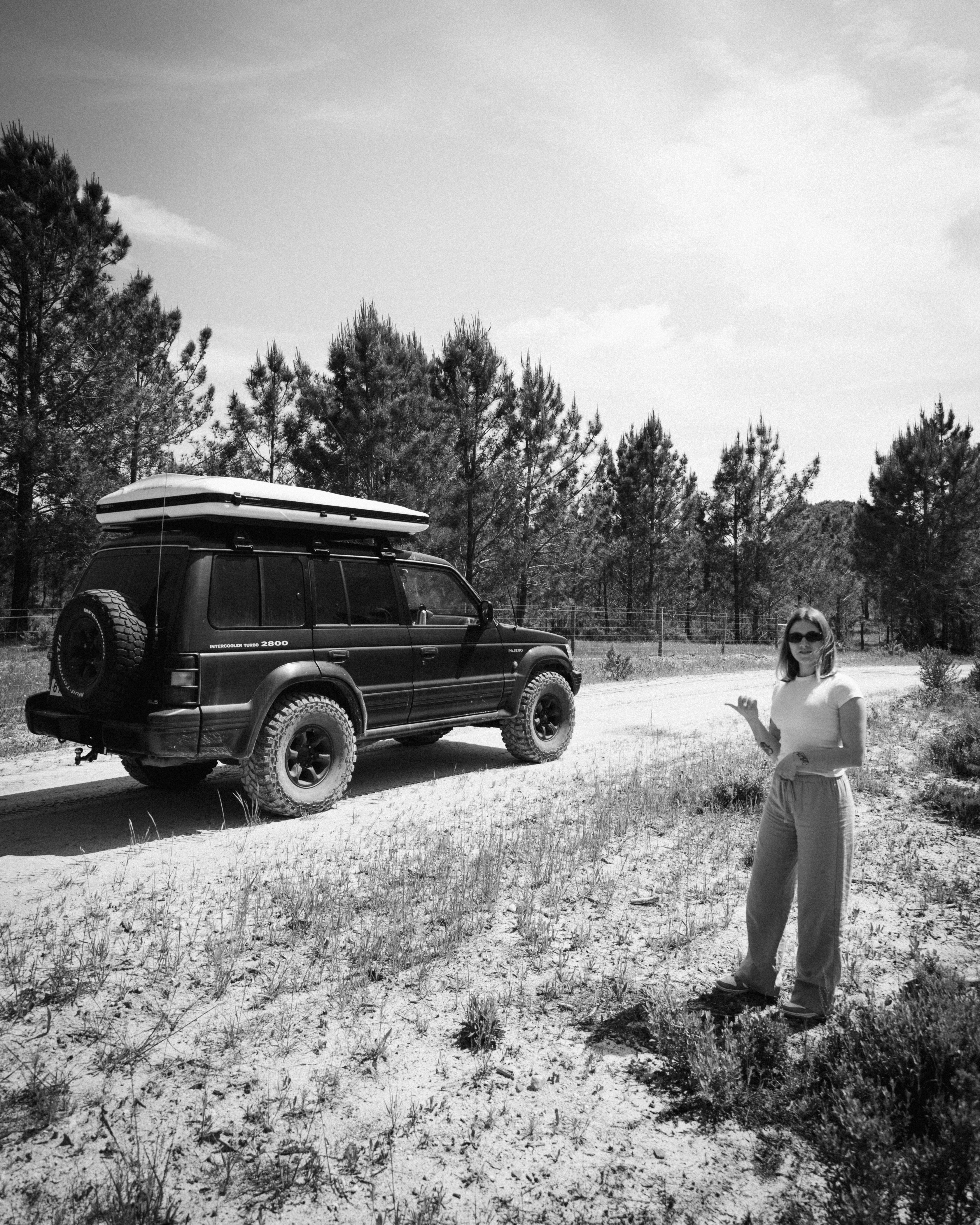 Dusty Road Portrait: Woman by a Rugged SUV in Sunlit Clearing