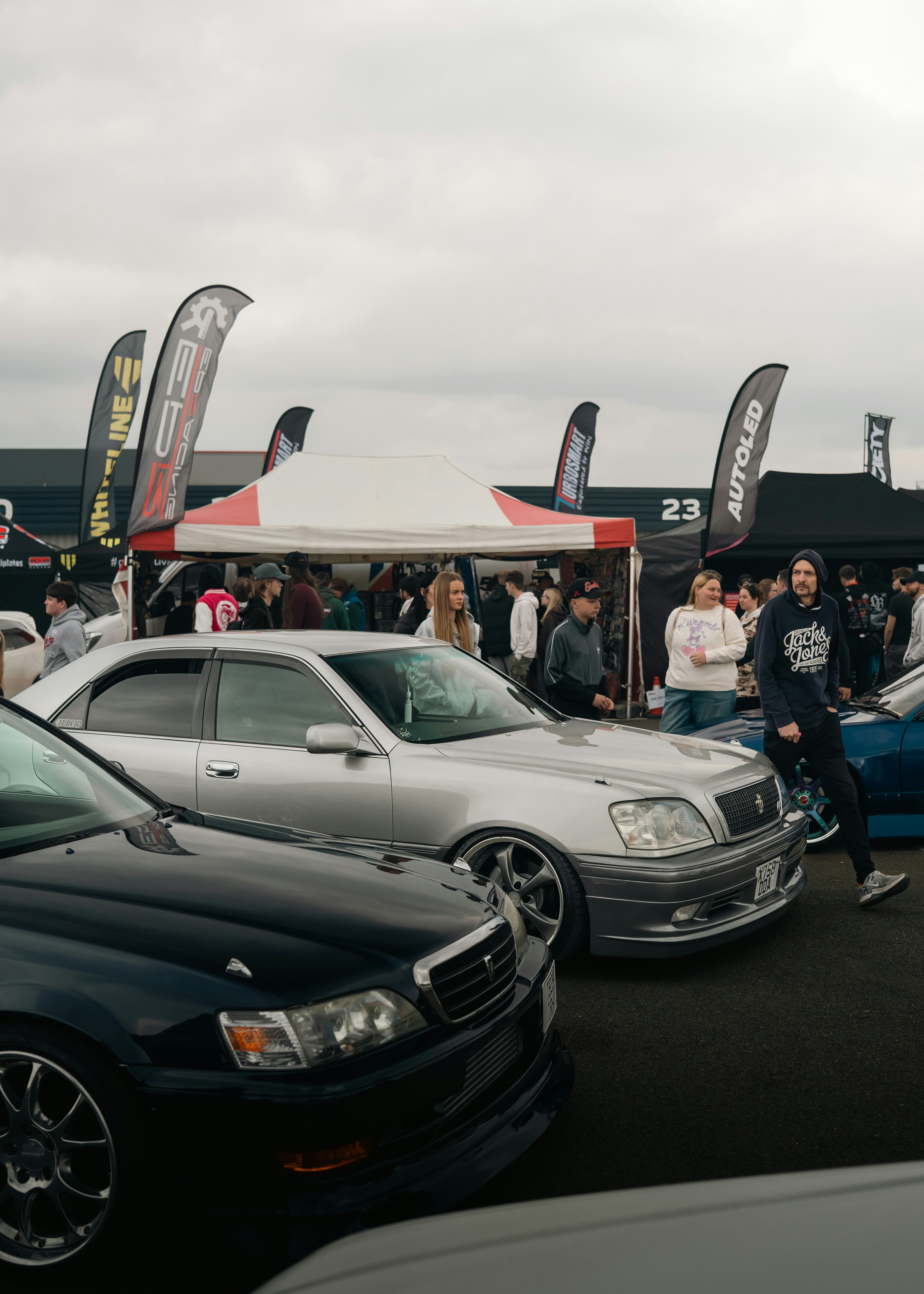 Cars and crowd under a striped tent at a car show