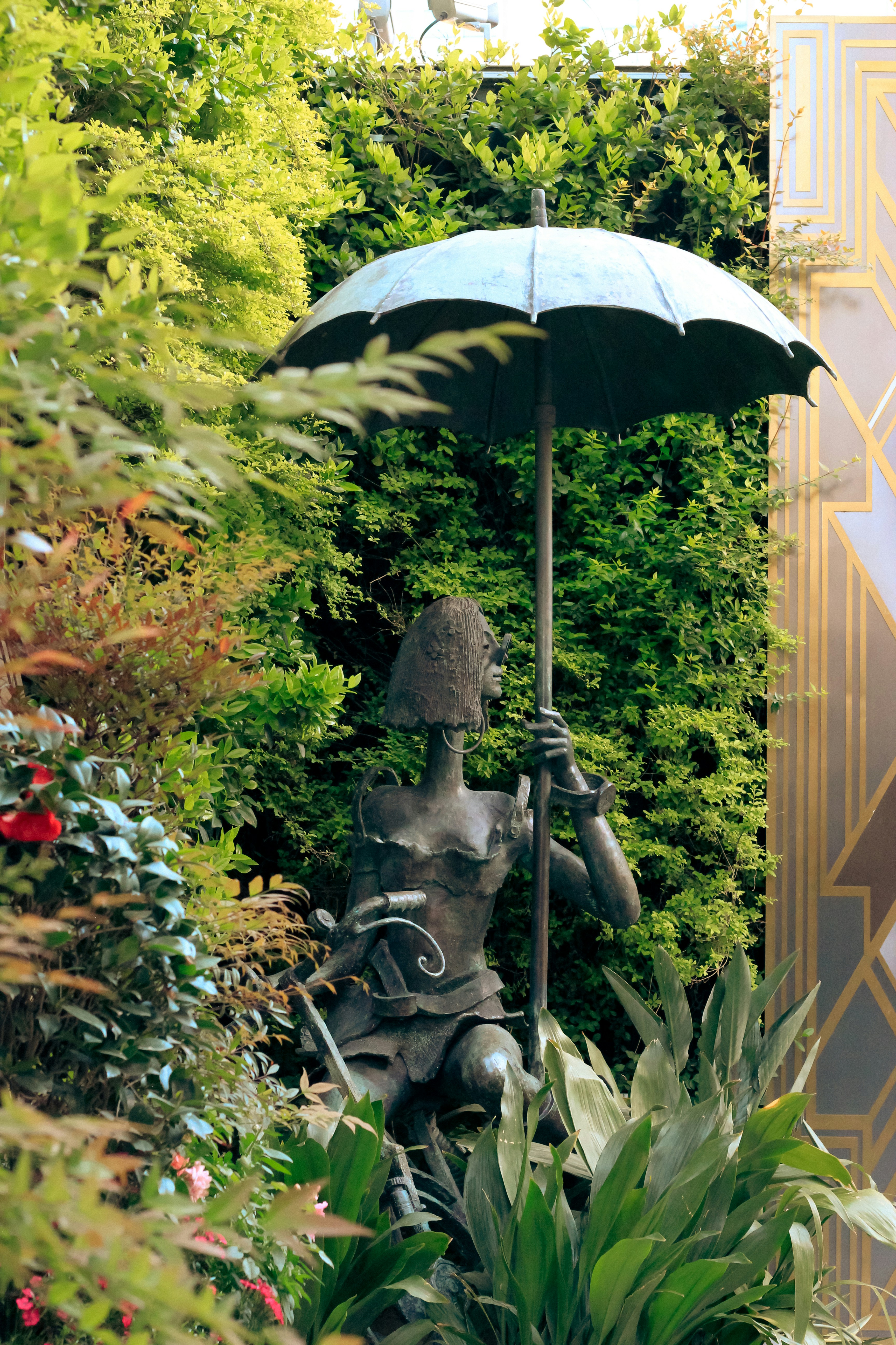 Statue in a Garden Seated under a Teal Umbrella