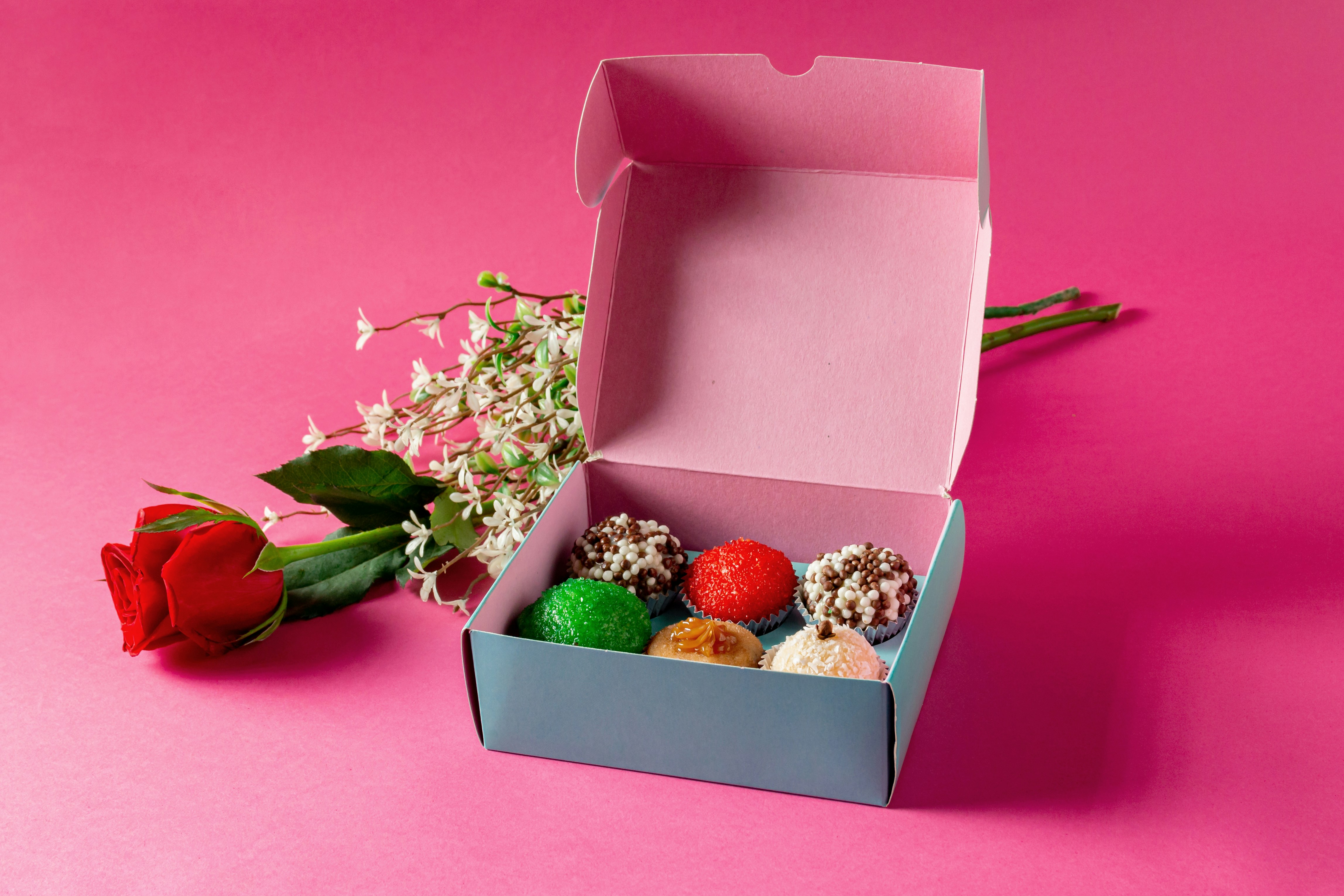 Box with Brazilian brigadeiro candy and red rose. Pink background.