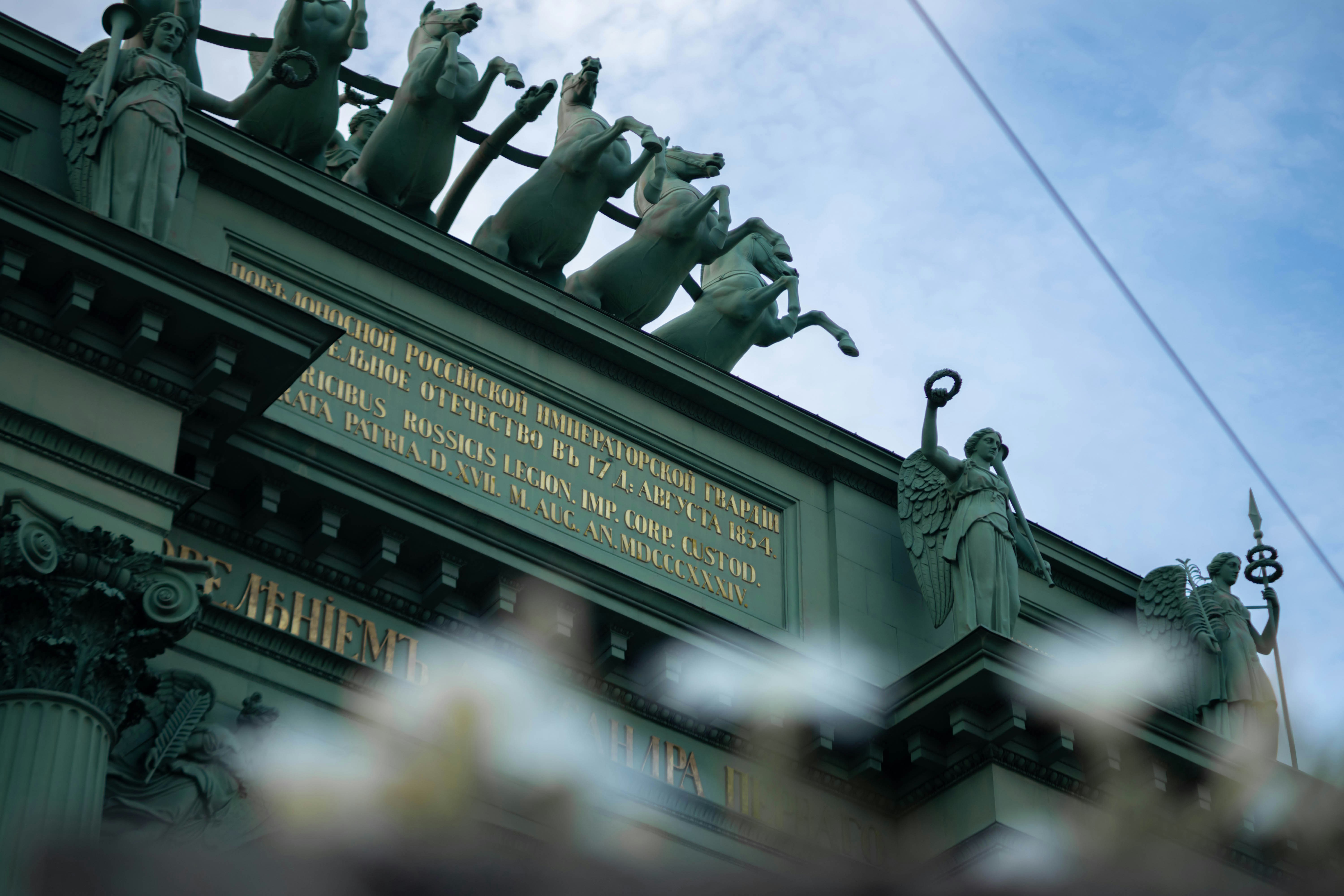 Statues atop a grand archway piercing a pale blue sky