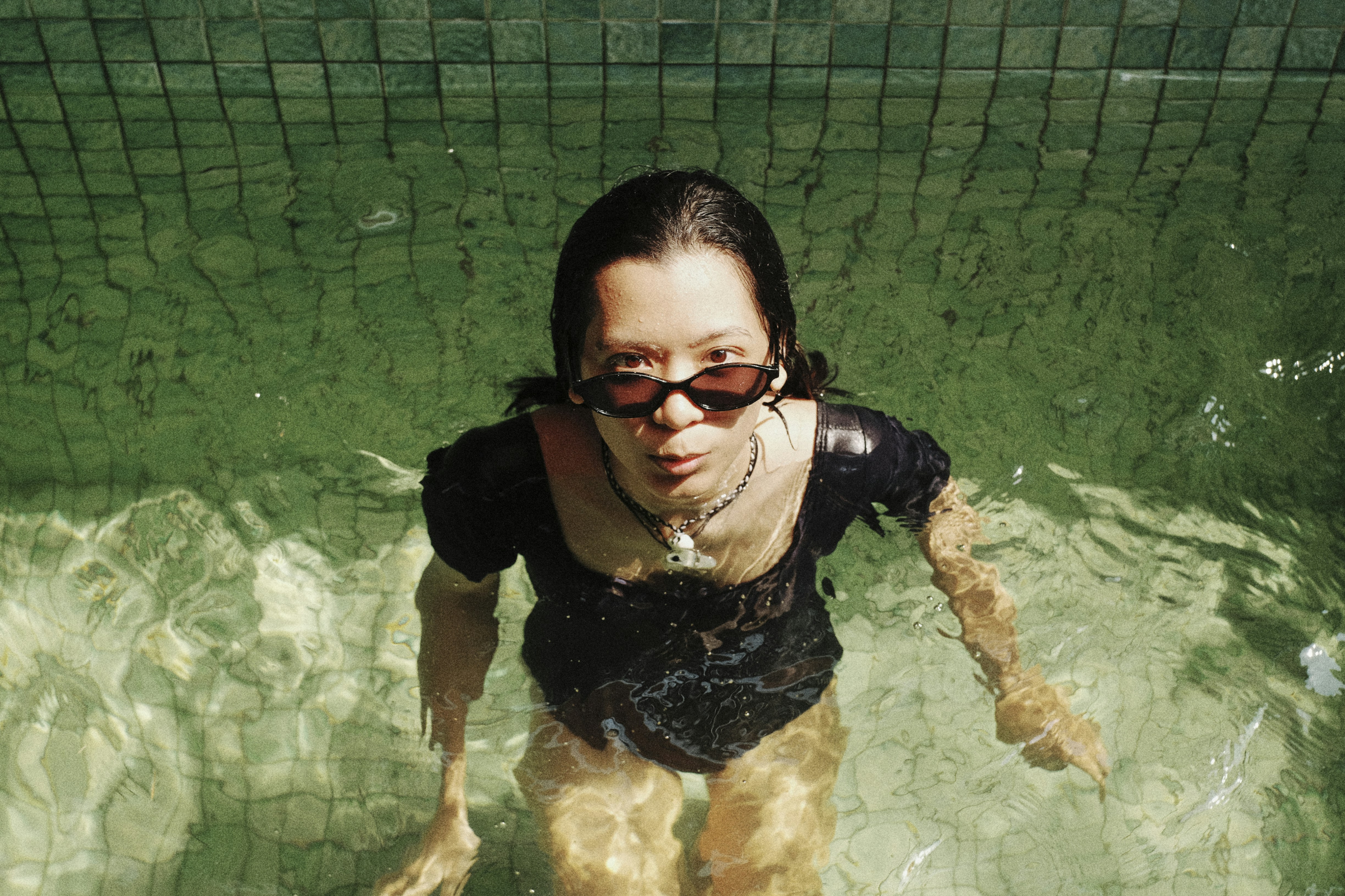 A girl wears sunglasses while swimming in a pool.