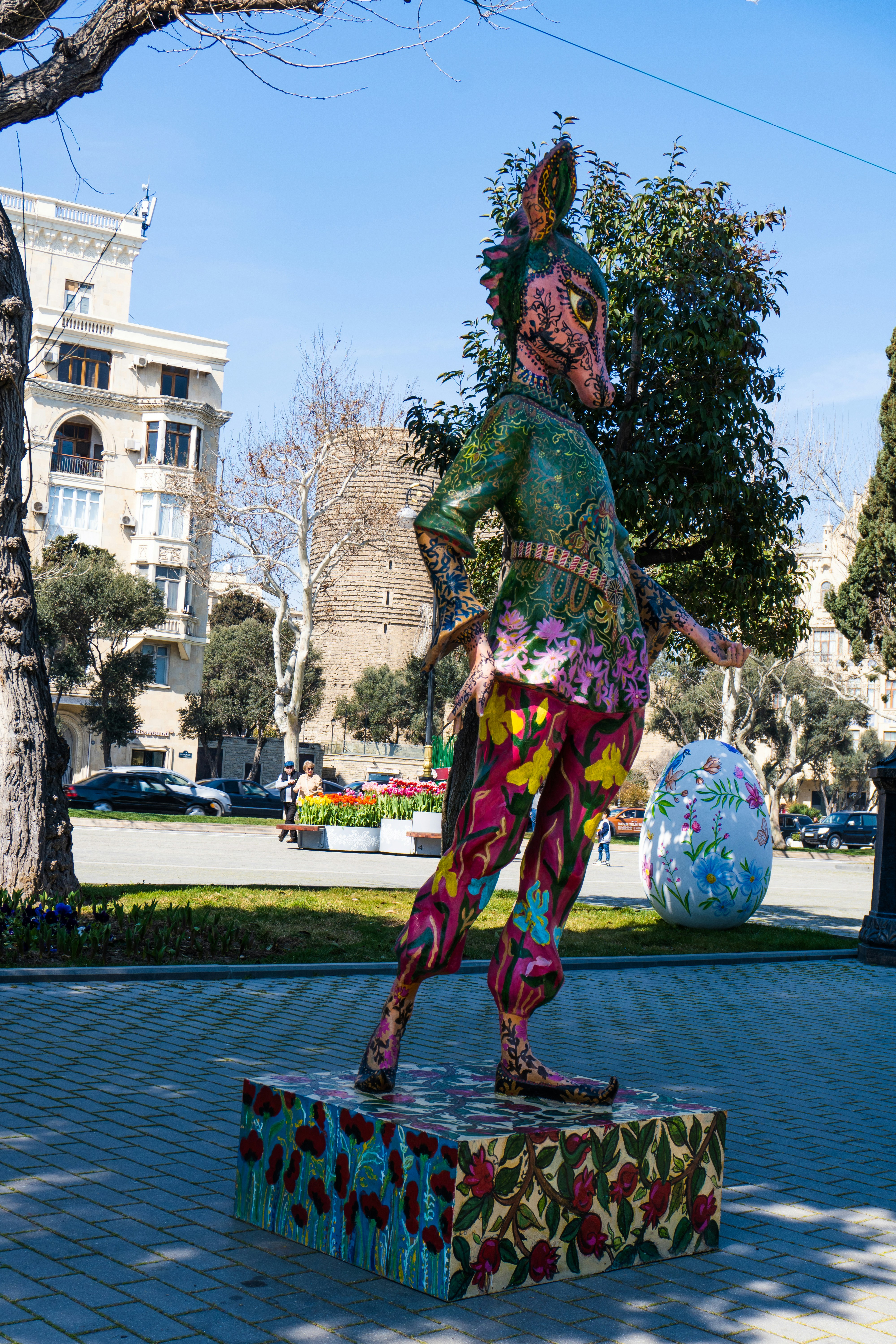 Dancing Giant in the City: A Colorful Parade Sculpture Balancing on a Floral Pedestal