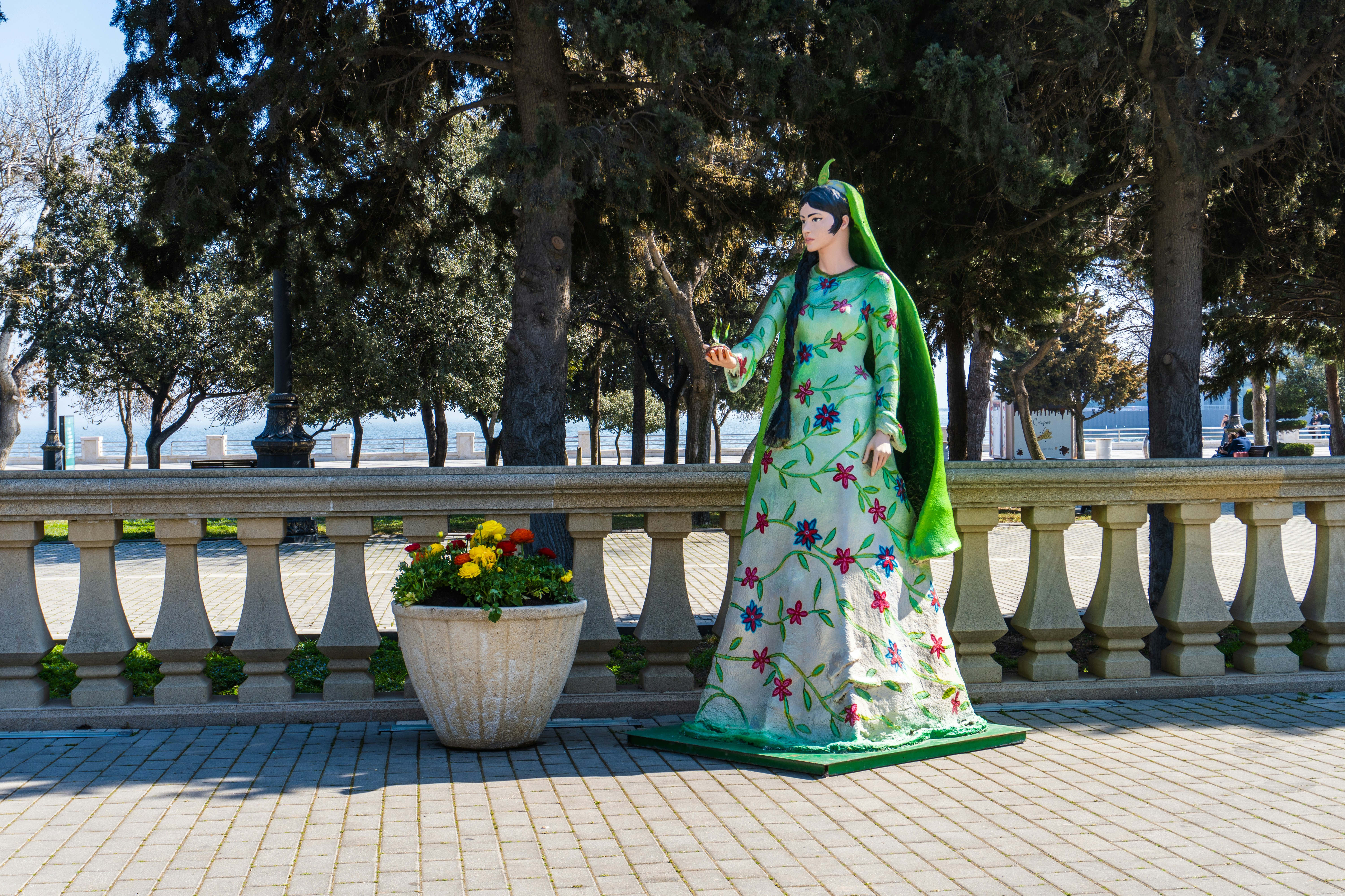Emerald-Draped Figure Stands Guard on a Sunlit Seaside Promenade