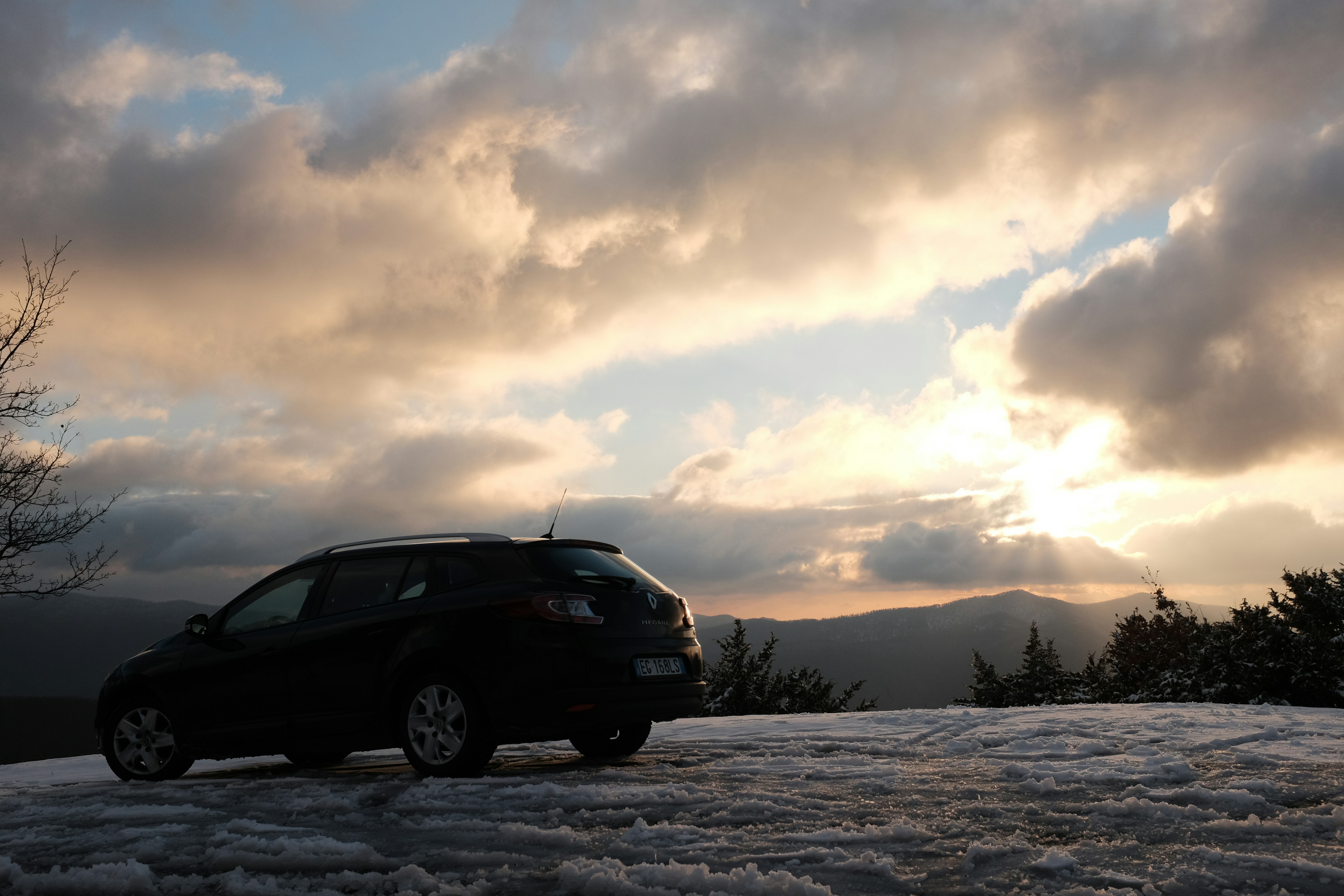 Dark SUV silhouette on a snow-covered hillside against a dramatic sunset sky.