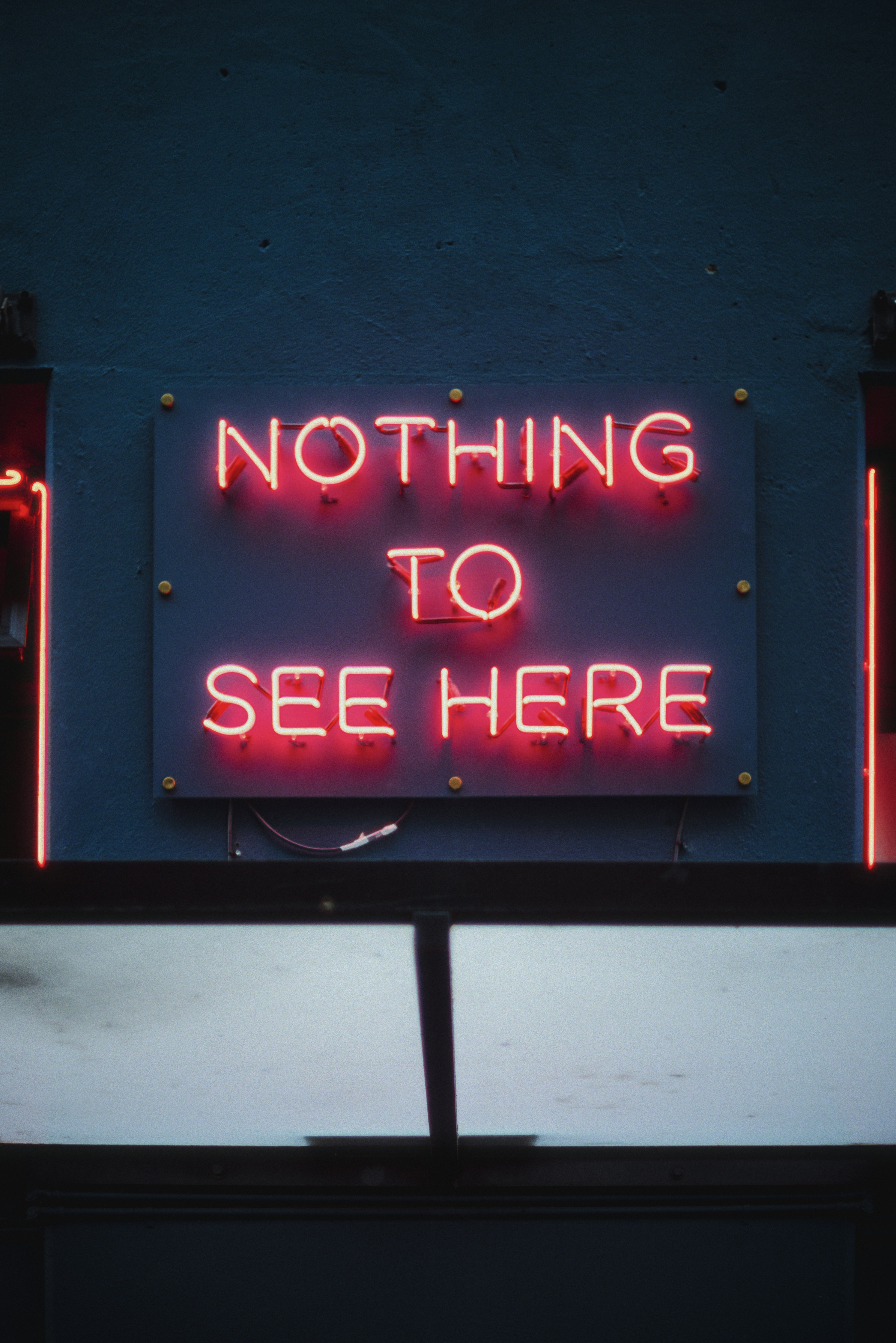 Neon sign reading 'NOTHING TO SEE HERE' against a blue backdrop, highlighting the contrast between message and visual appeal.