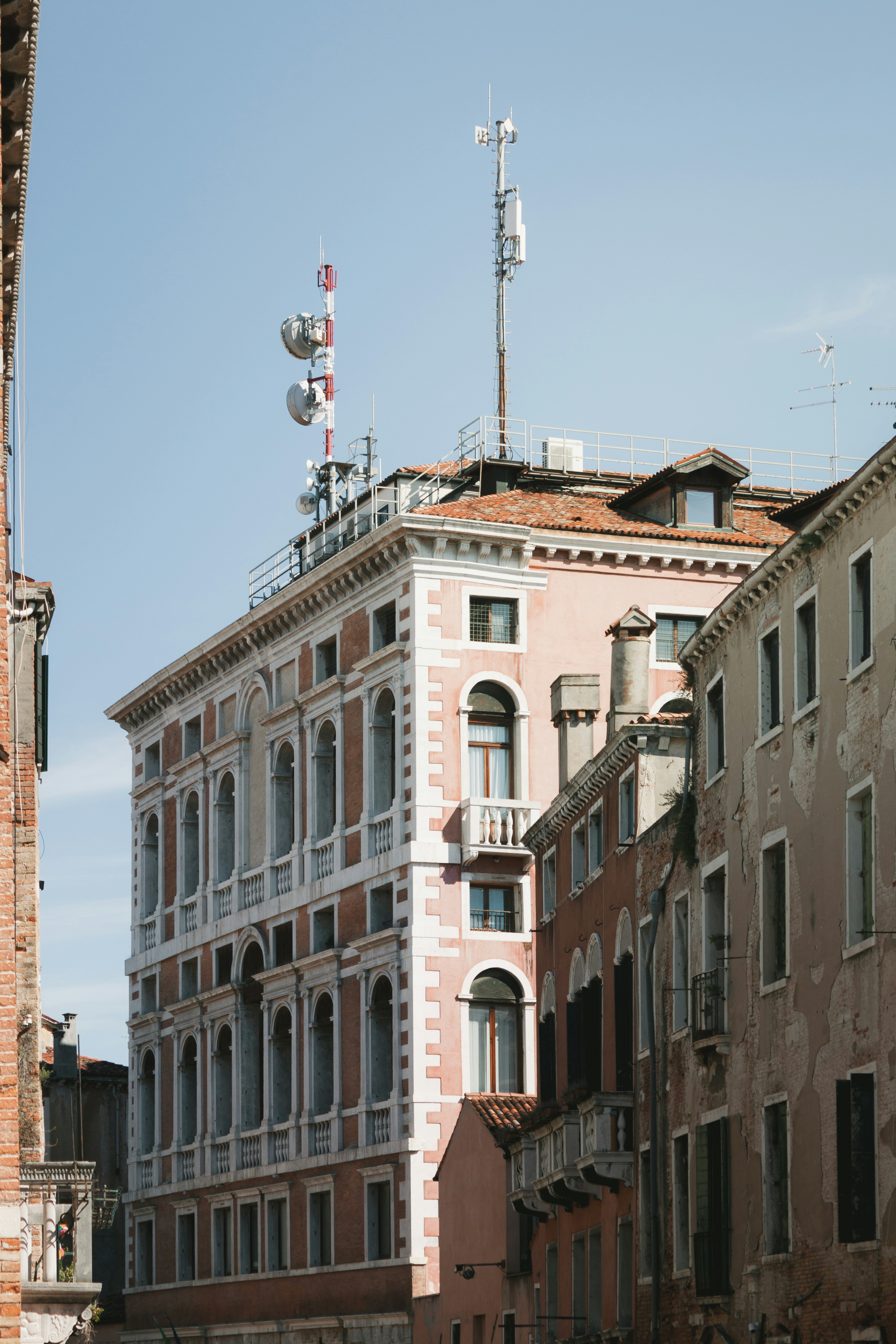 Pastel Palazzo: Arched Windows and Antenna Crown on a Sunlit Street